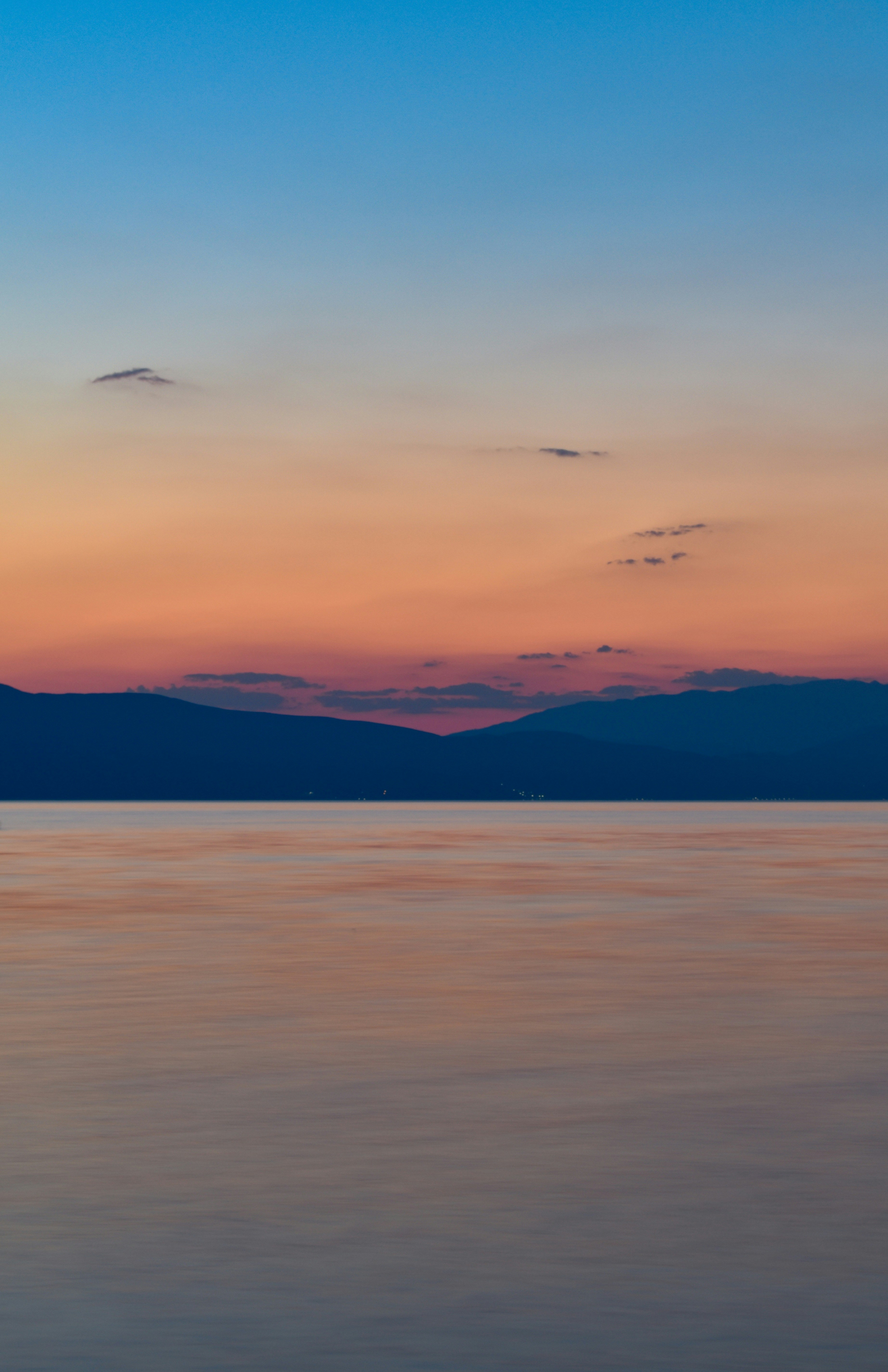 Serene twilight scene featuring a calm lake reflecting soft hues of blue and pink, framed by distant mountains. The tranquil atmosphere invites contemplation.