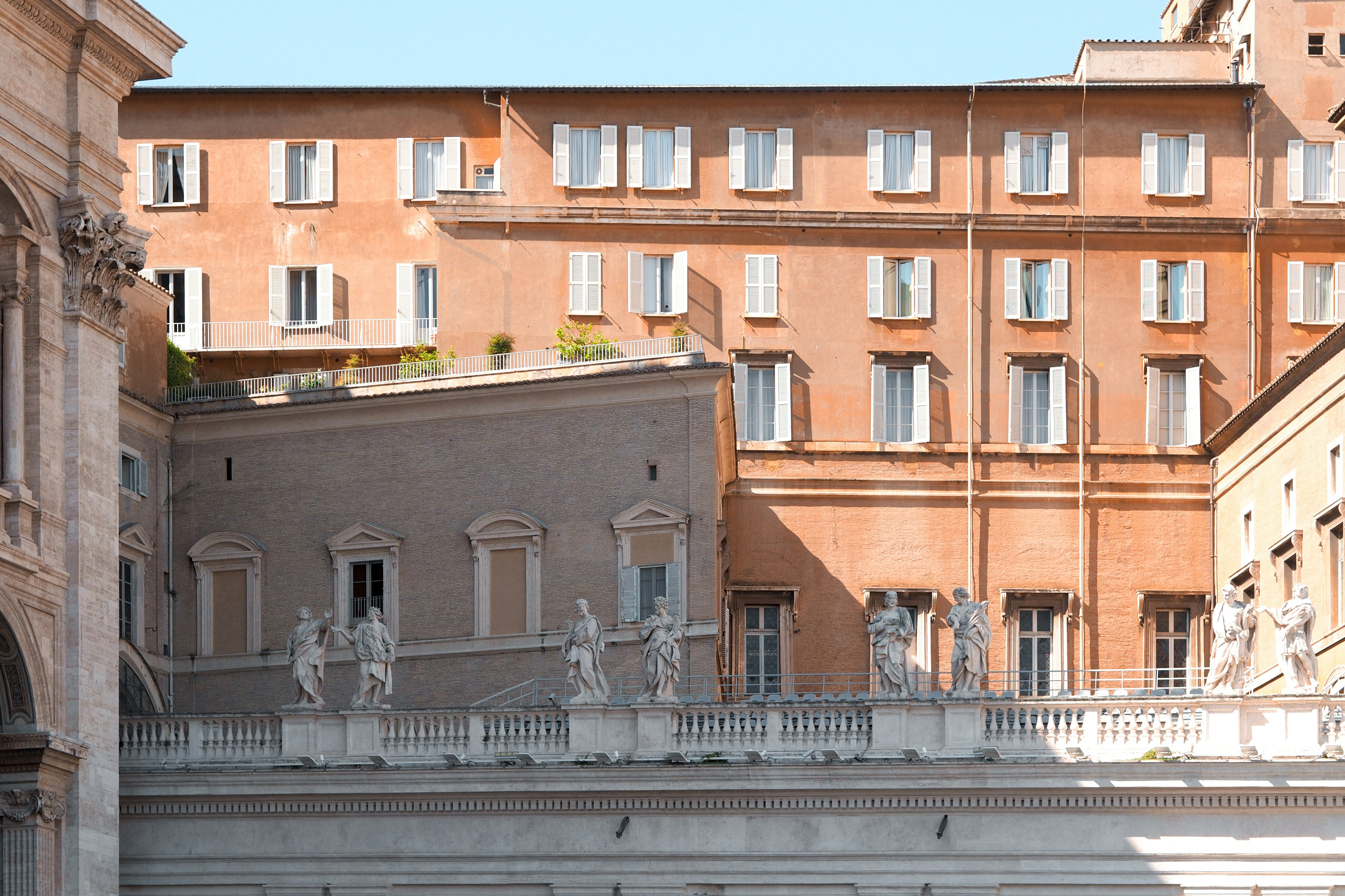Elegant sculptures line the rooftop of a historic building, contrasting with the modern windows of adjacent structures. The interplay of light and shadow emphasizes architectural details.
