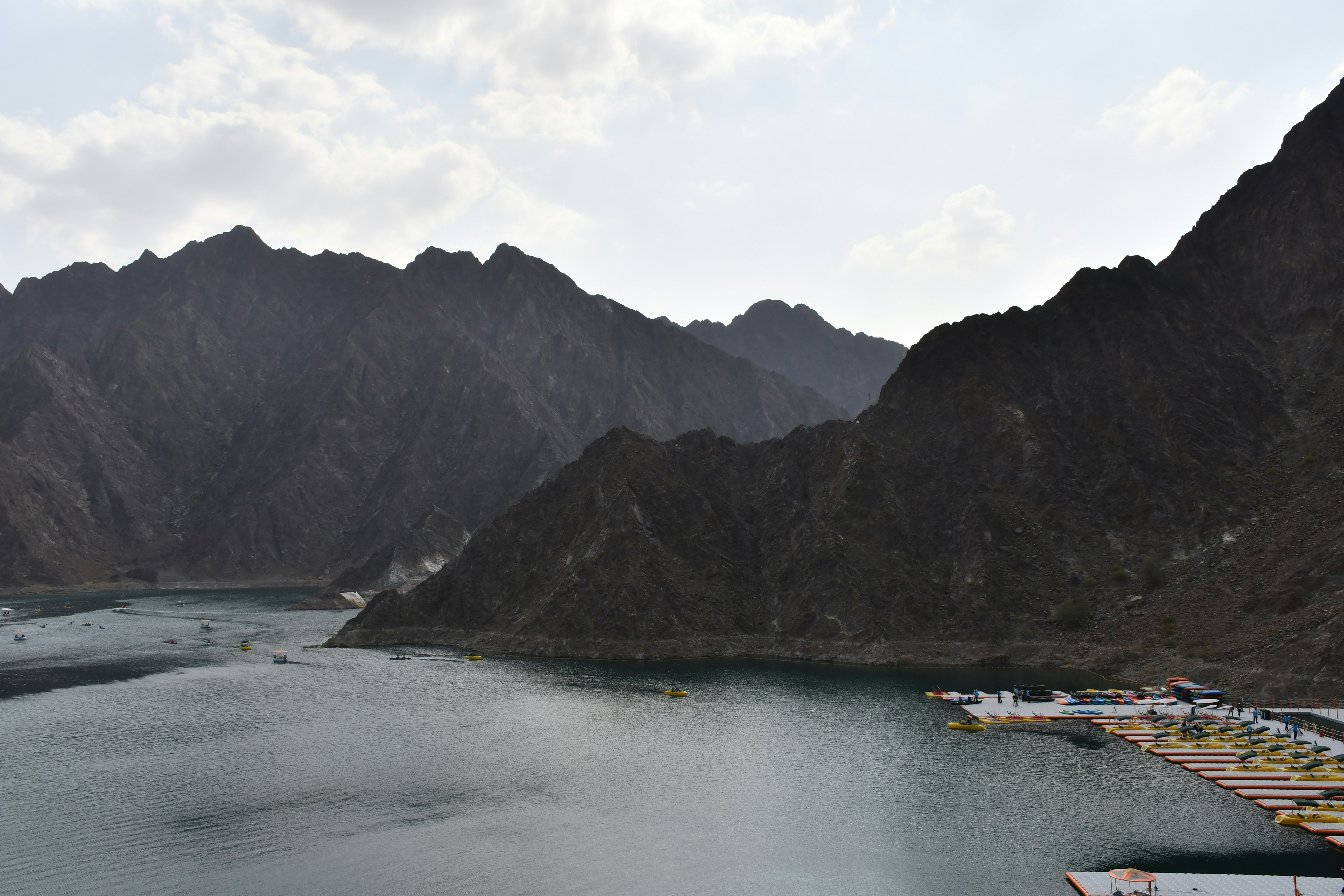 Serene waters reflect rugged mountains, dotted with colorful boats along the shore. The landscape captures the tranquility of nature's embrace.