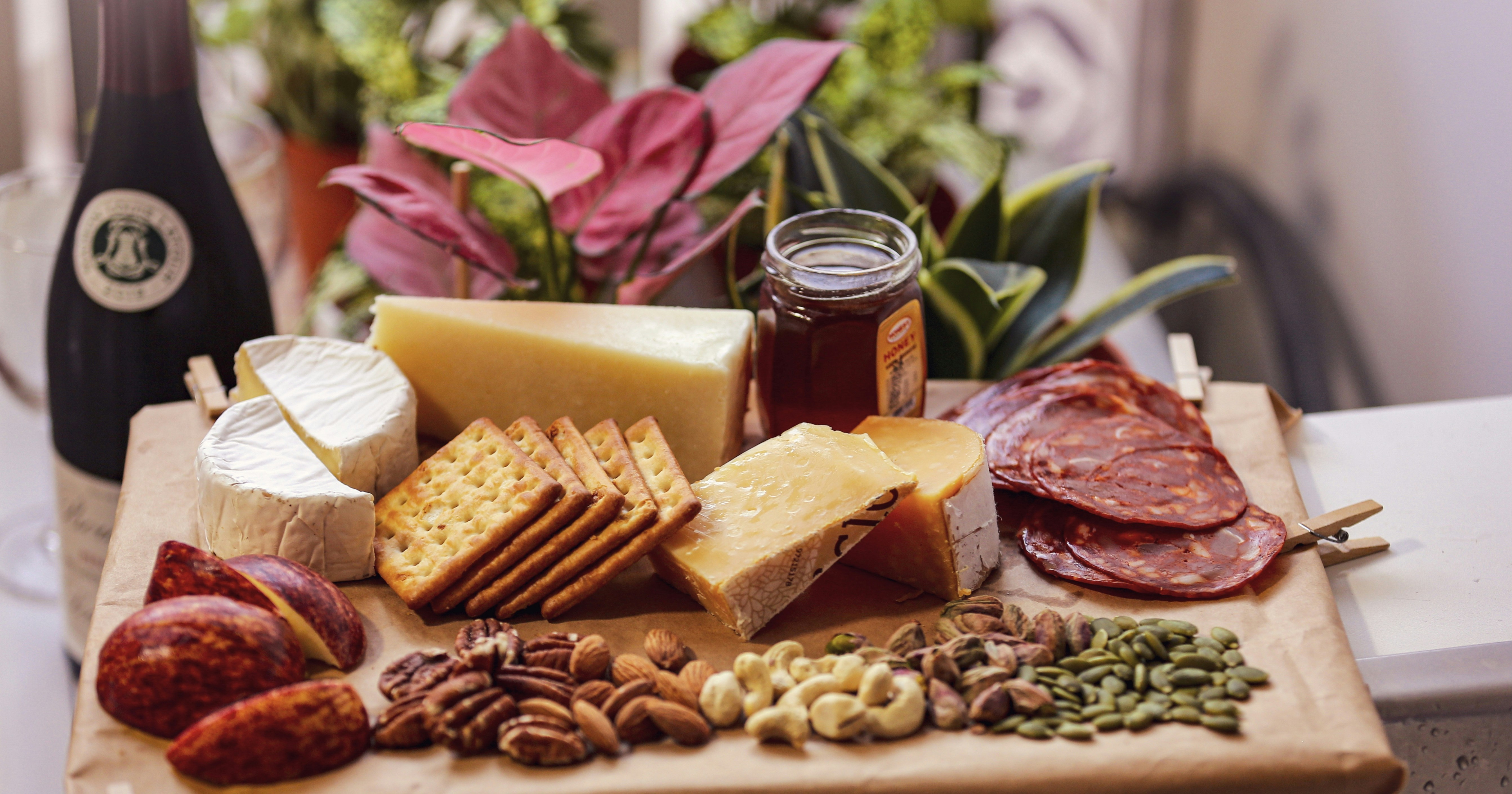 An inviting charcuterie board featuring assorted cheeses, cured meats, nuts, and honey, beautifully arranged with vibrant greenery in the background.