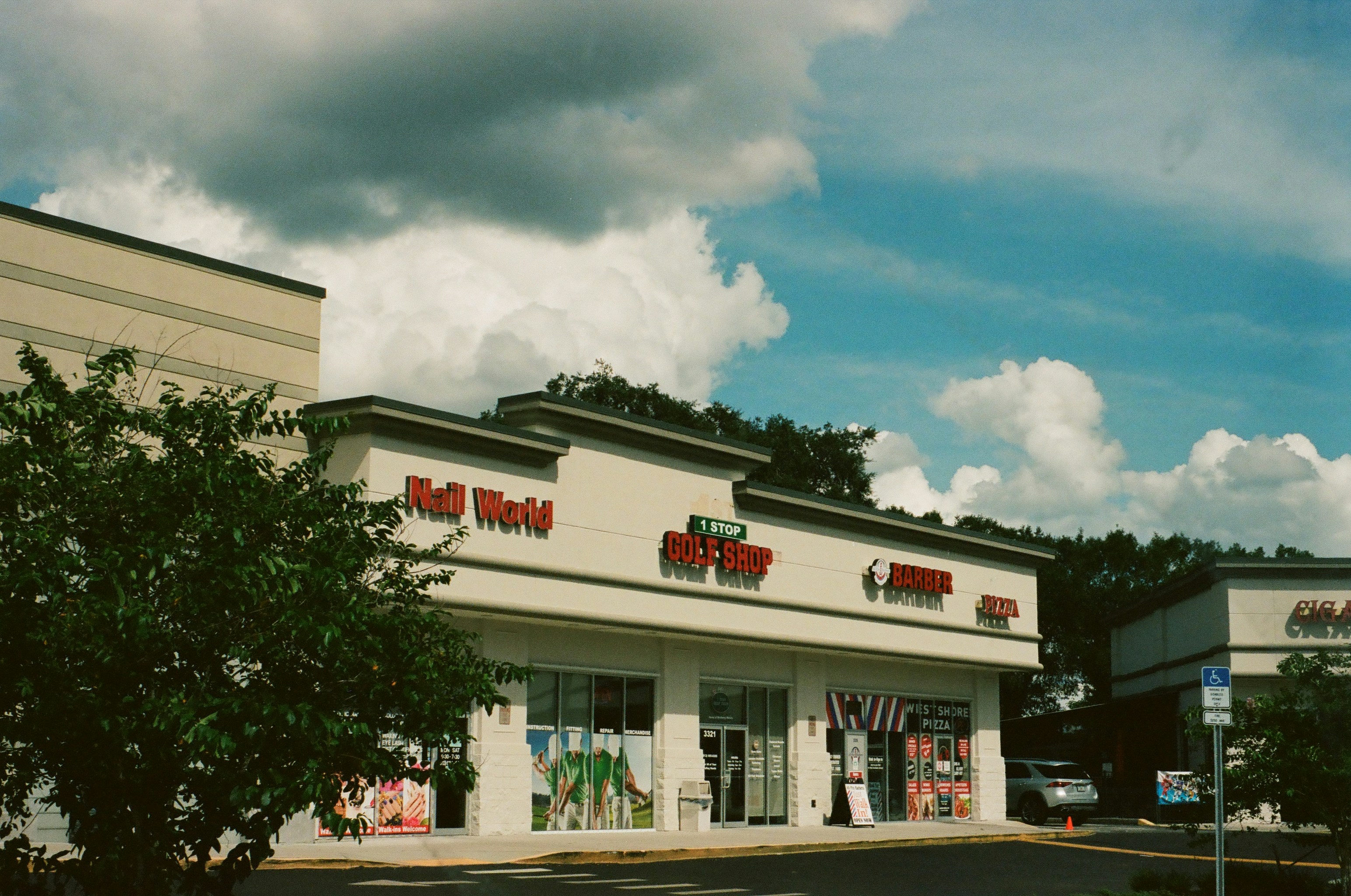 Golf shop exterior showcasing vibrant signage and merchandise, framed by lush greenery and a dramatic sky.