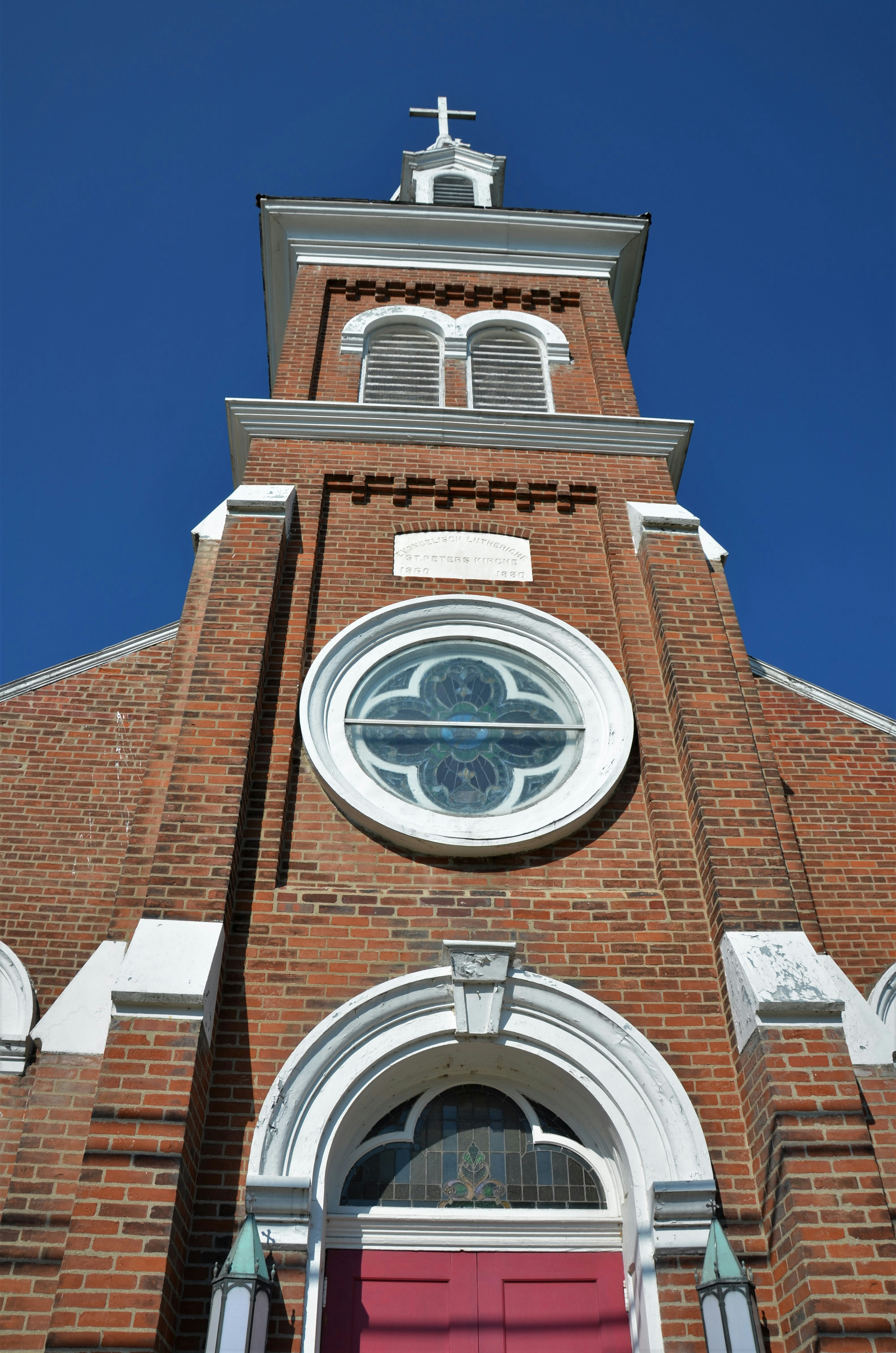 Historic church facade showcasing intricate brickwork and a prominent circular stained glass window, framed by a clear blue sky.