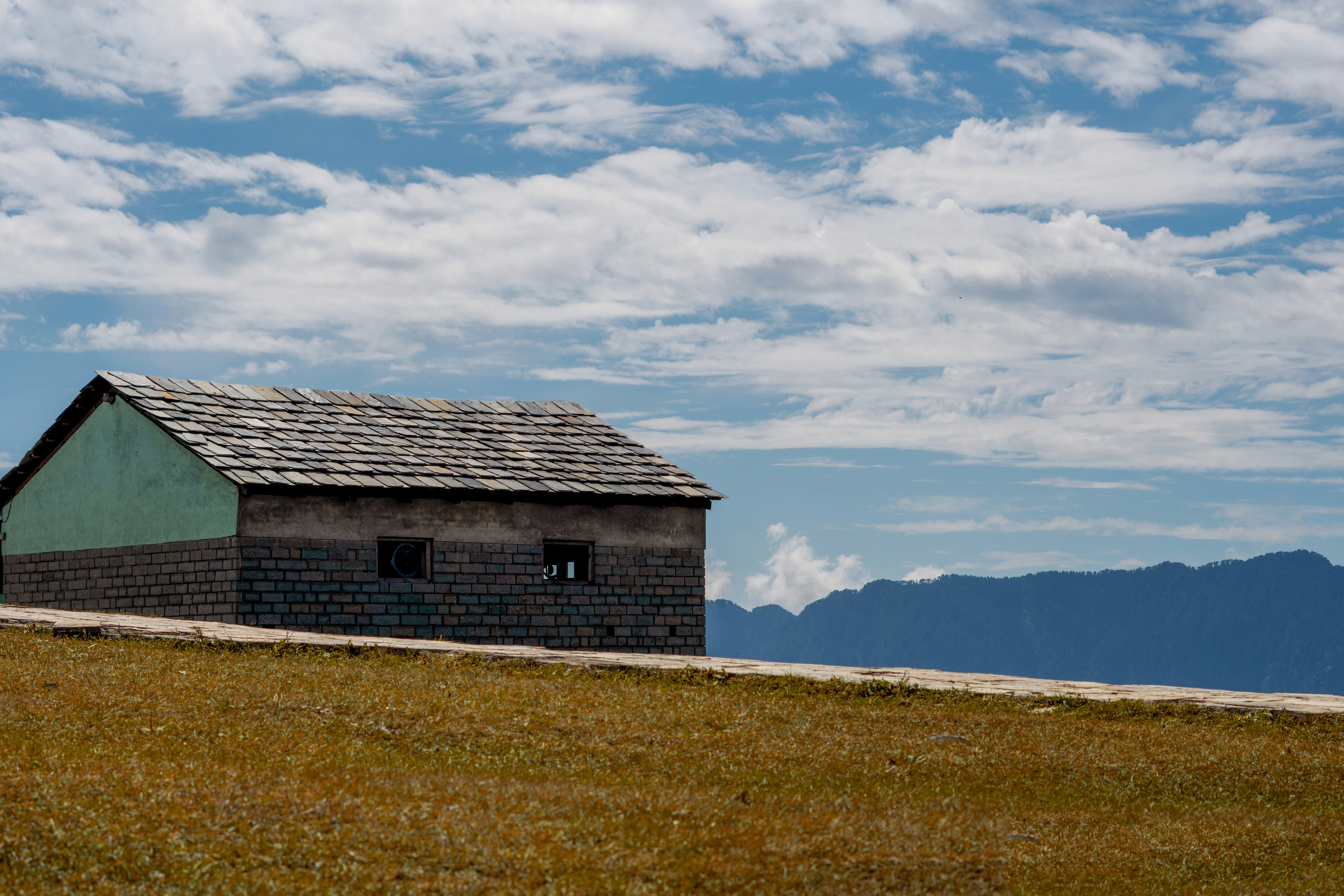 black wooden house on green grass field under white clouds and blue sky during daytime