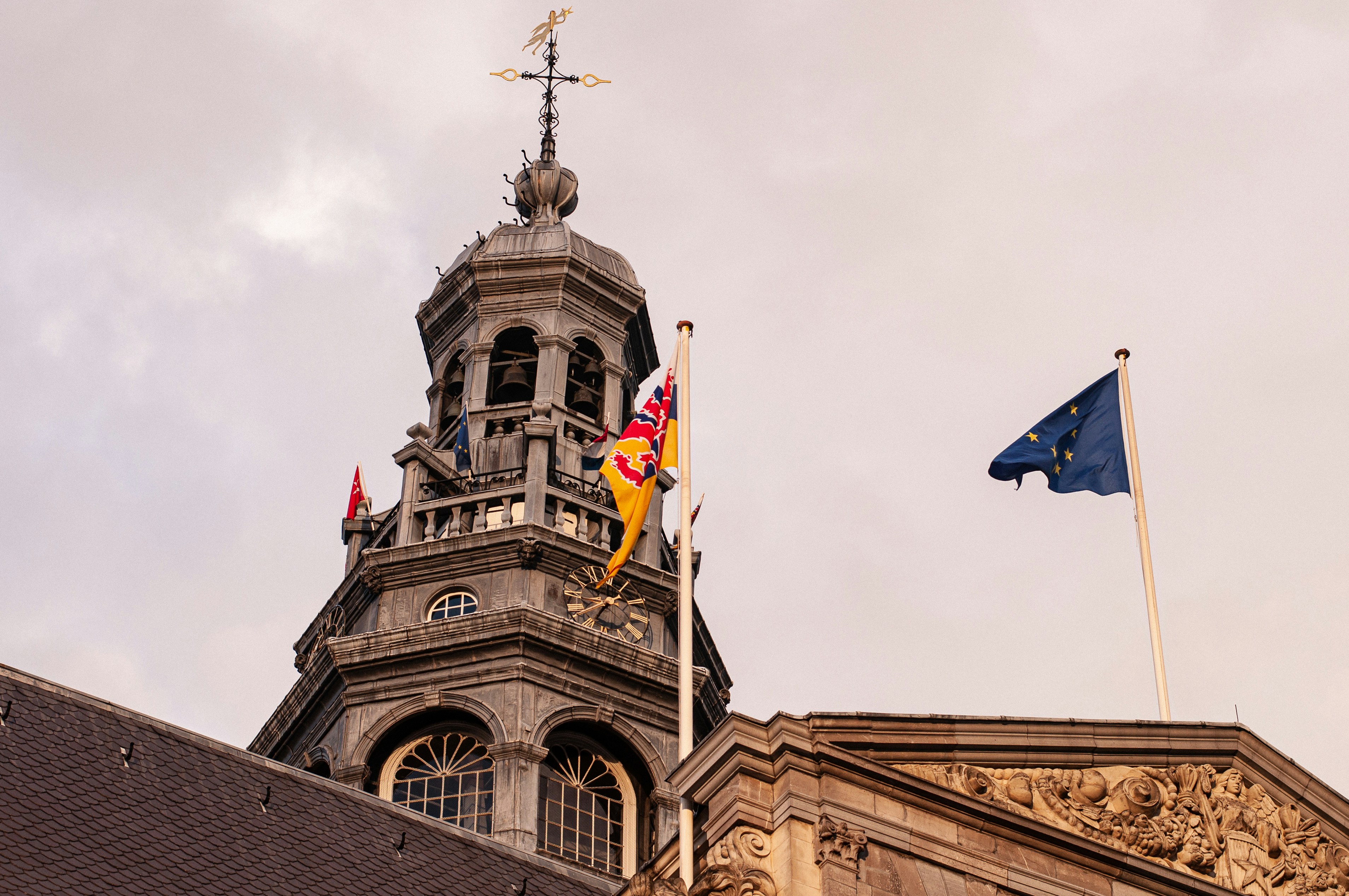 Historic clock tower adorned with flags against a pastel sky, showcasing architectural elegance.