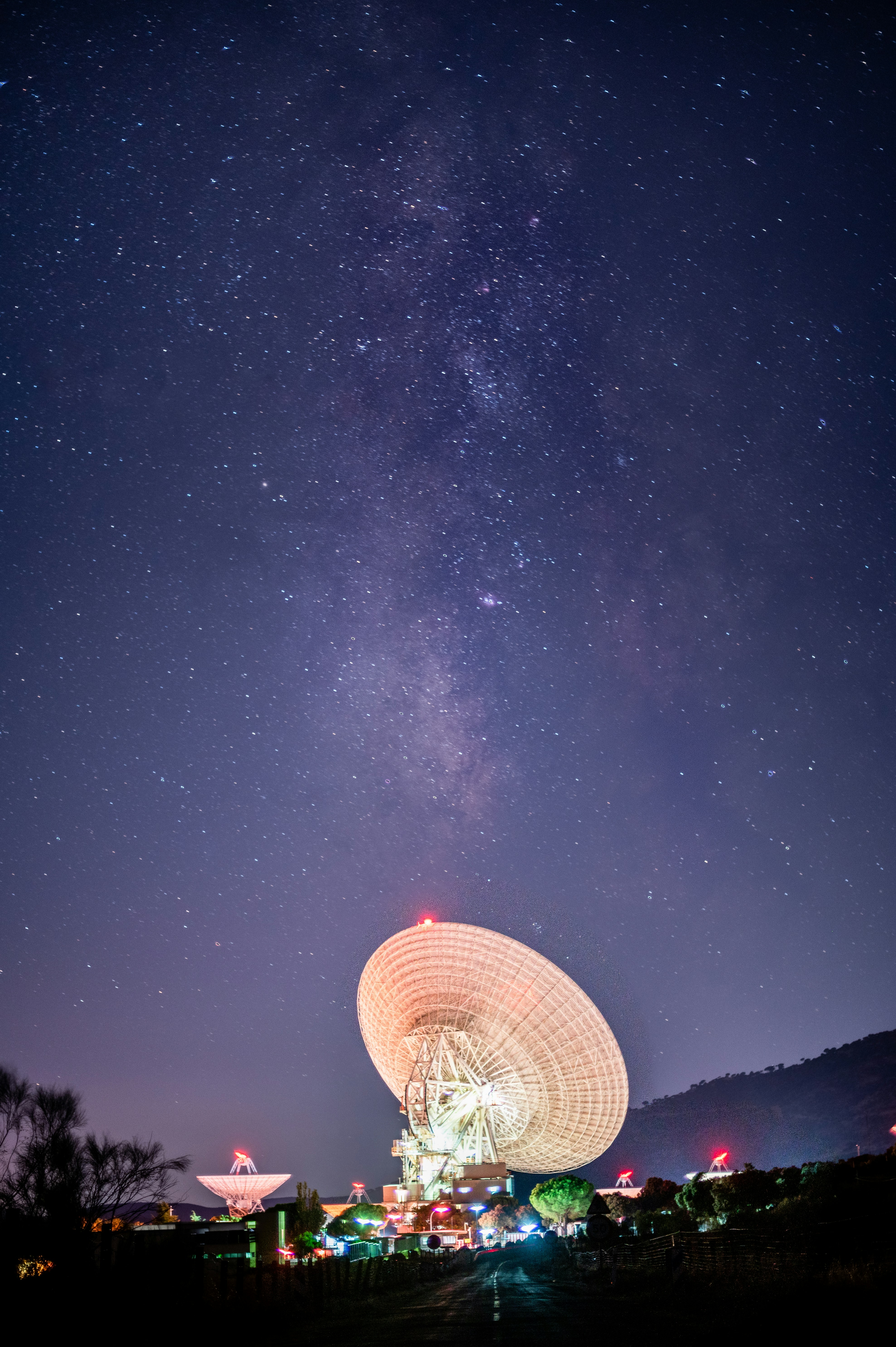Large radio telescope under a starry sky, with the Milky Way visible above. The scene captures the intersection of astronomy and technology.