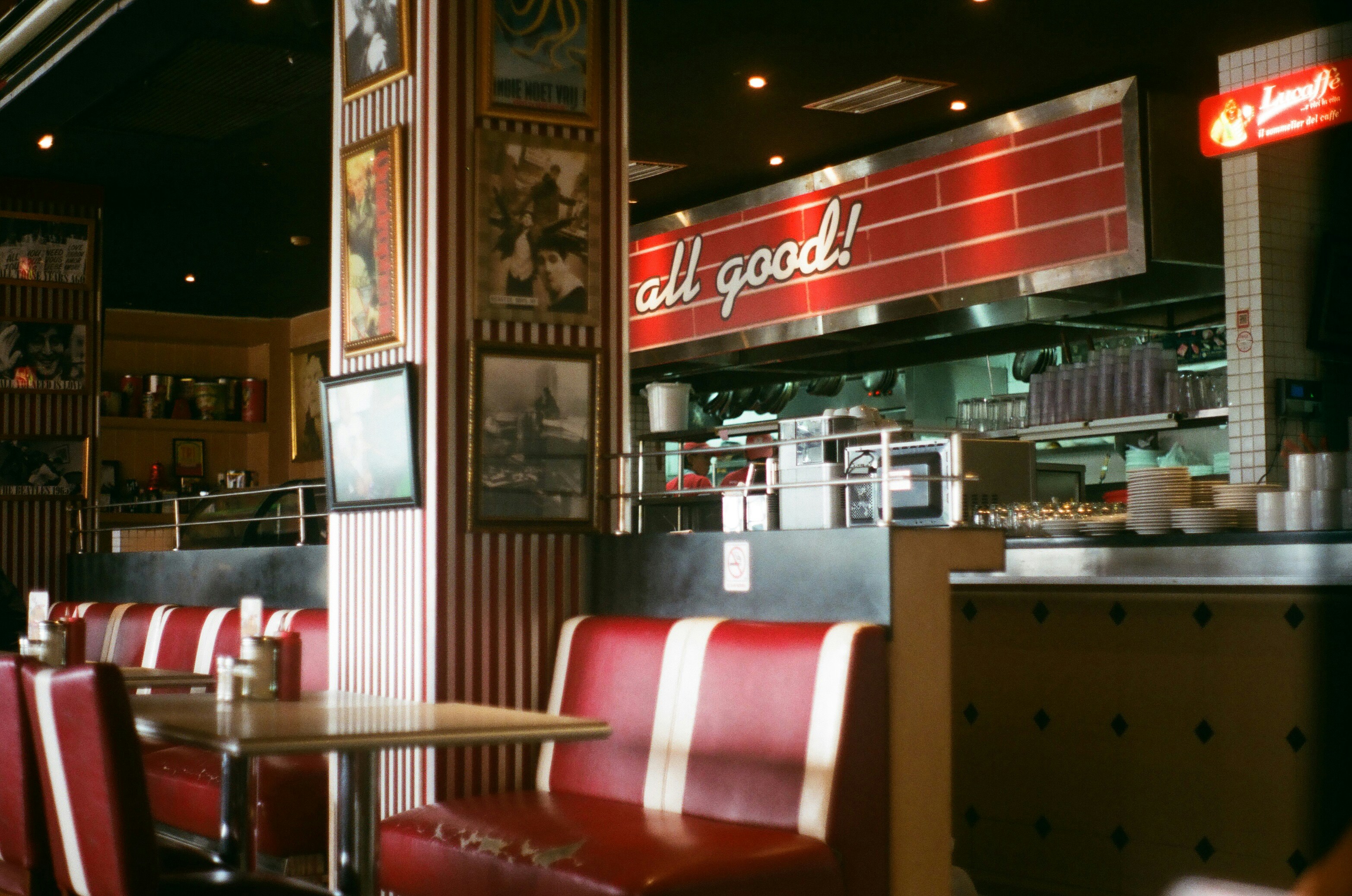 Cozy diner interior featuring red and white striped seating, vintage decor, and a bustling kitchen in the background. Bright neon signage adds to the nostalgic atmosphere.