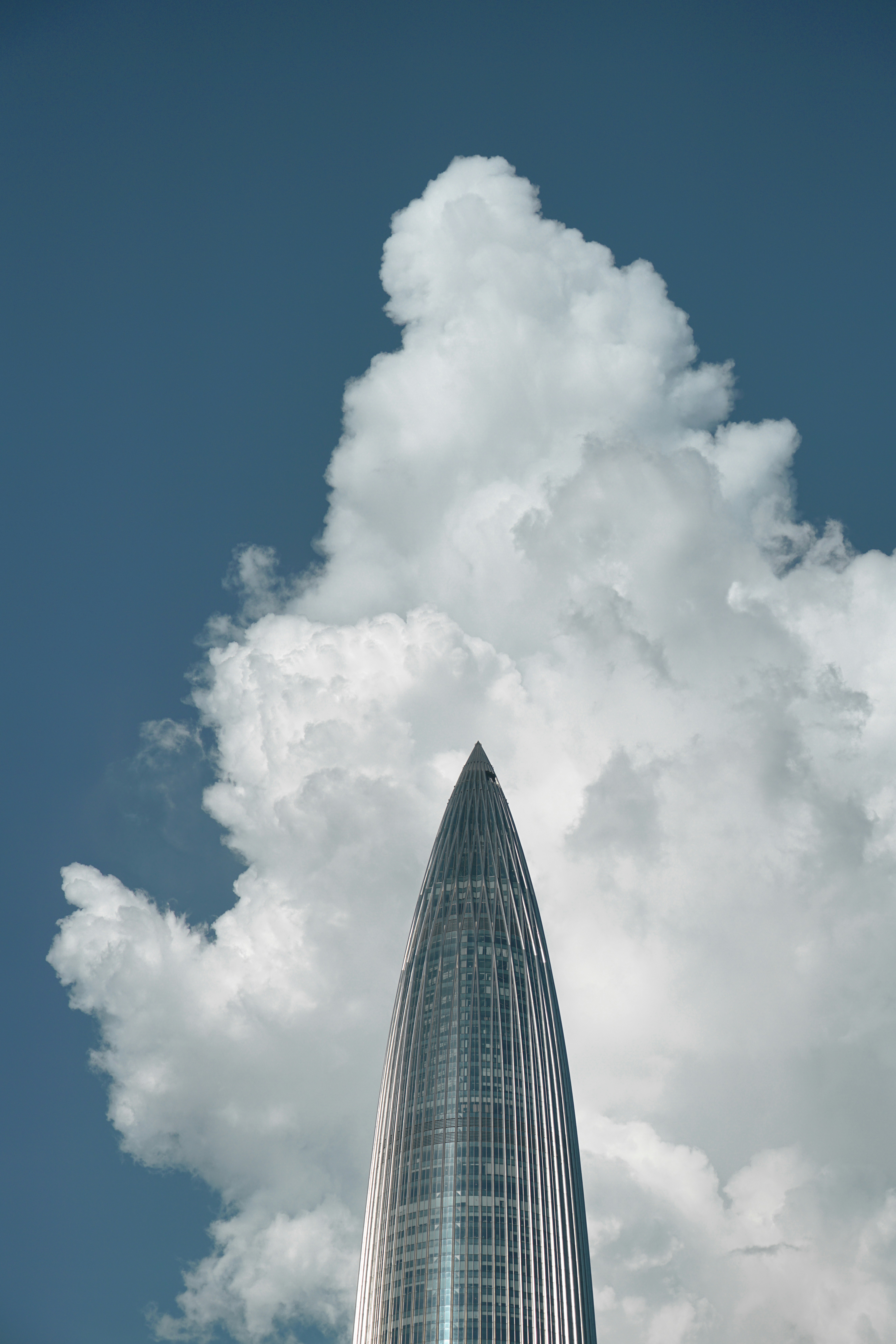 A sleek skyscraper rises sharply against a backdrop of fluffy clouds, showcasing modern architecture and nature's beauty.
