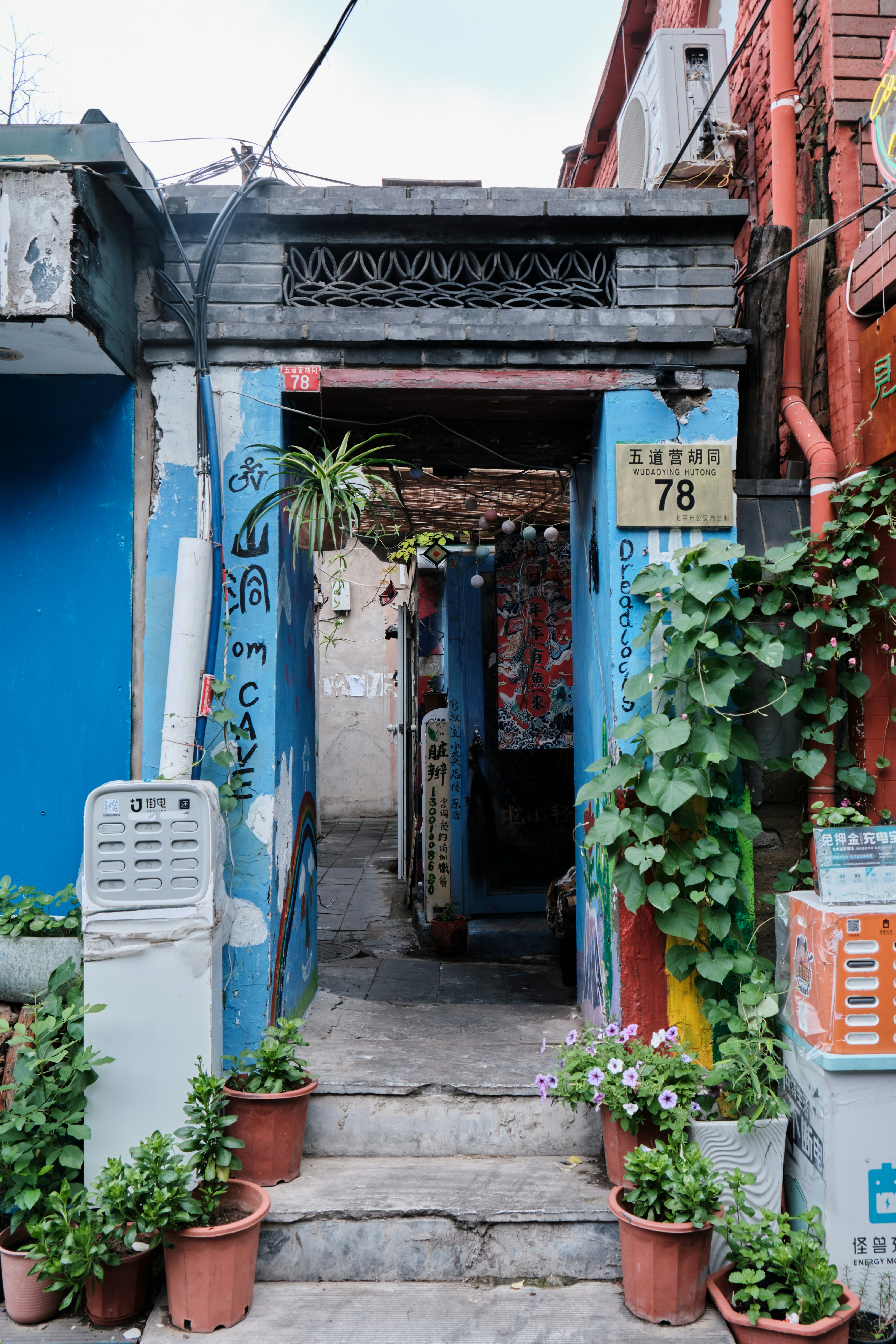 Colorful alleyway adorned with murals and greenery, leading to an inviting entrance marked by the number 78.