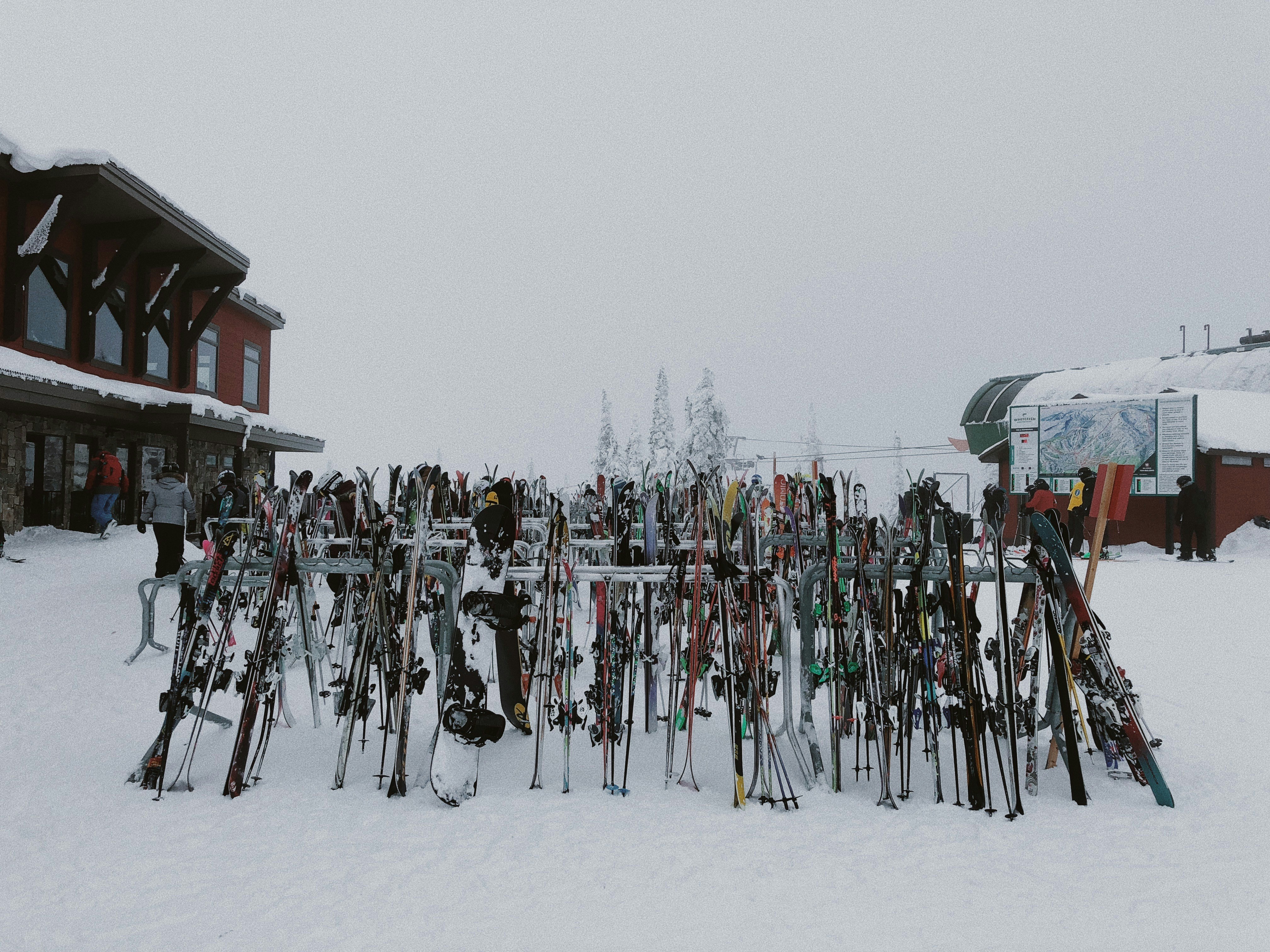 A bustling ski rack filled with various skis and poles, set against a snowy backdrop and a foggy sky. The scene captures the essence of a winter sports hub.