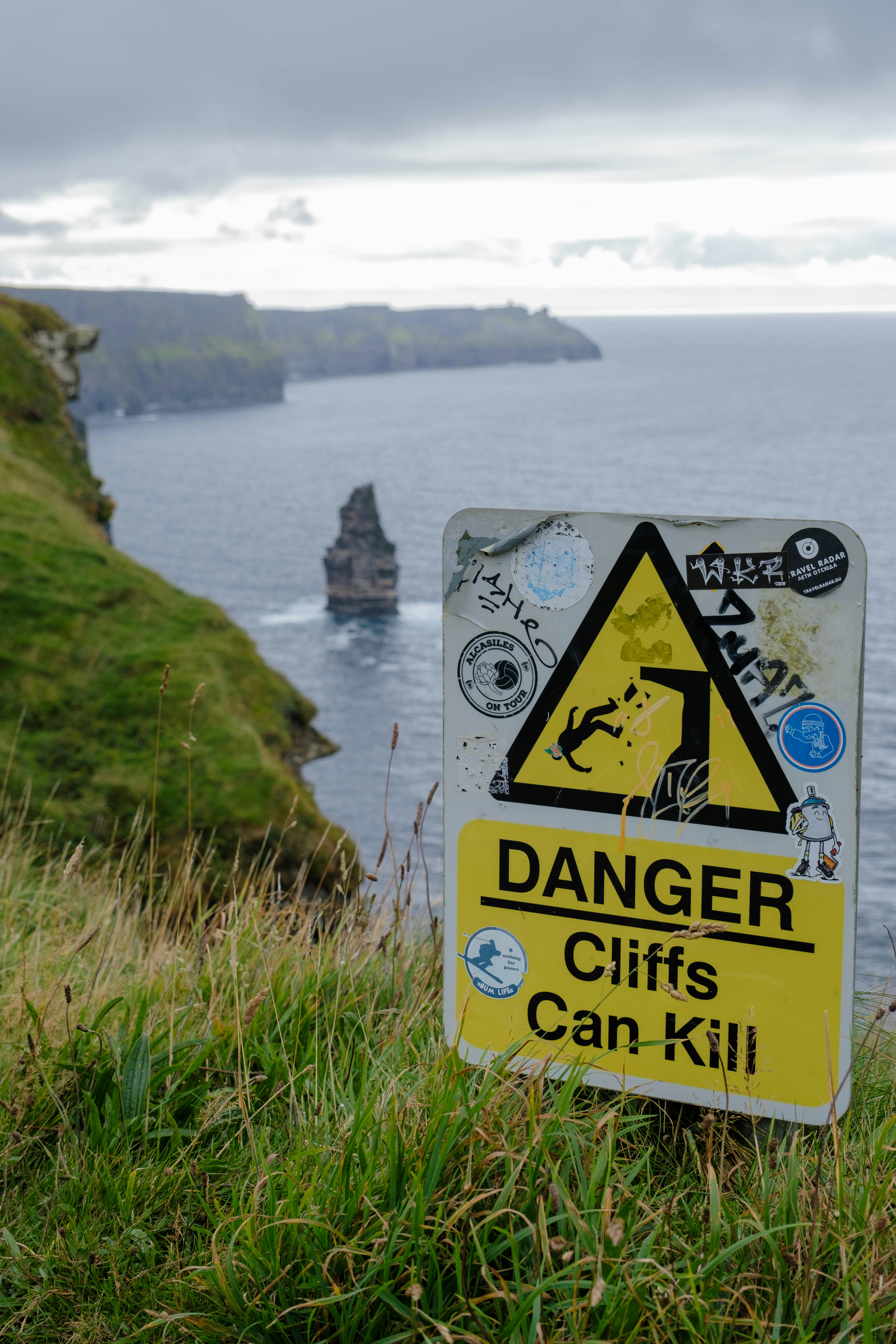 a vandalized warning sign in front of the Cliffs of Moher in Ireland