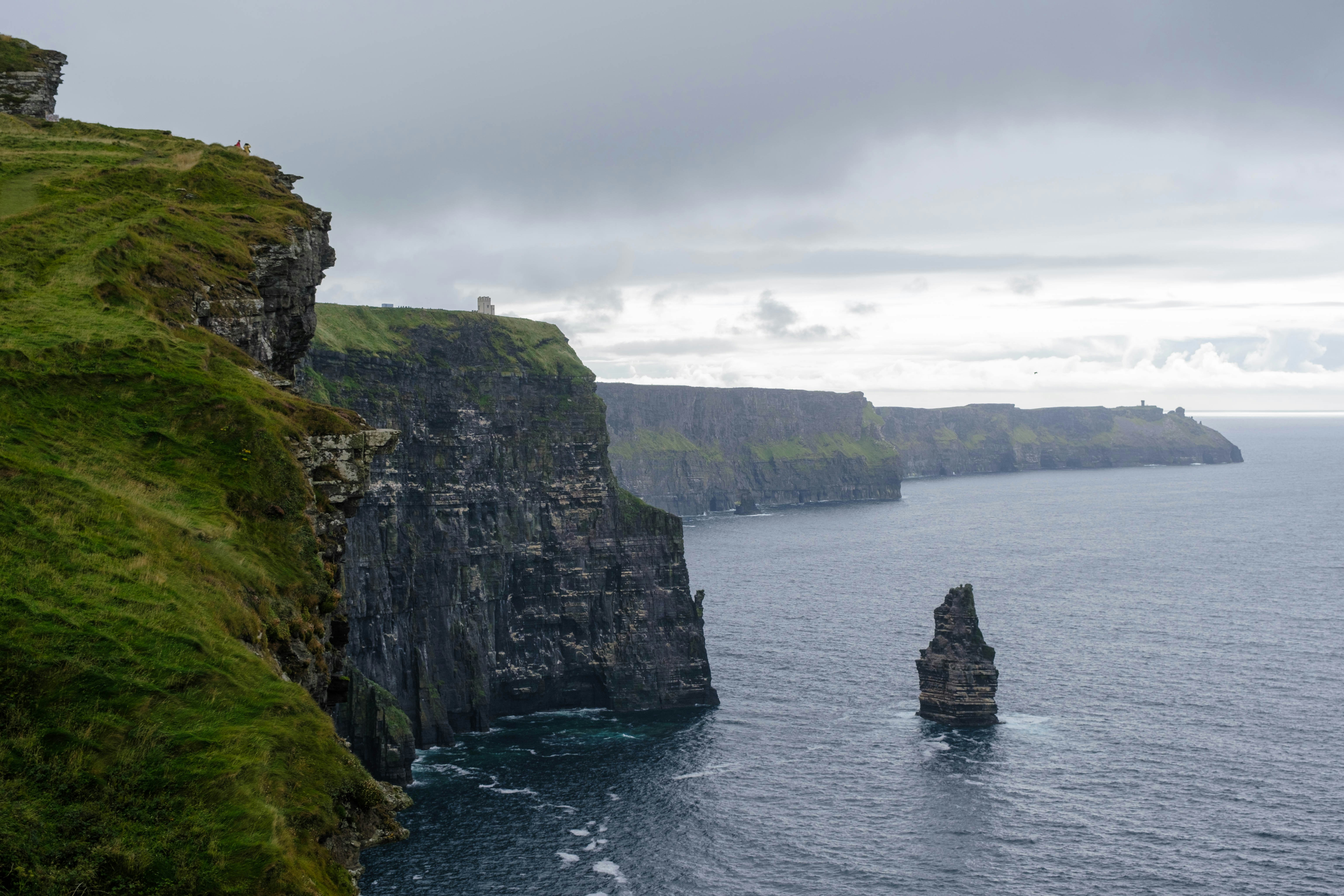Dramatic rocky cliffs rise above the Atlantic Ocean under a cloudy sky.