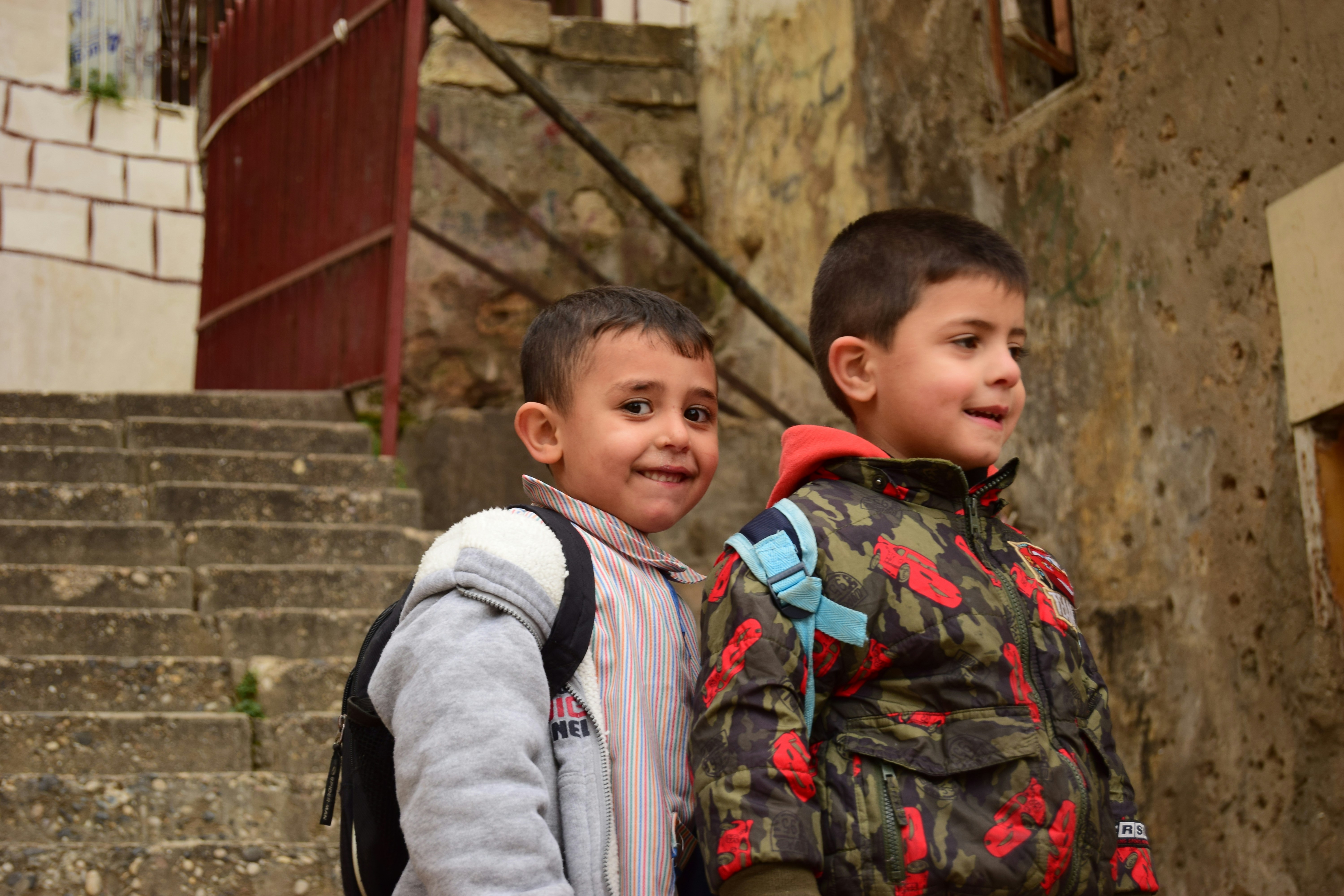 Two children in colorful jackets playfully standing on a stone staircase in an old neighborhood.