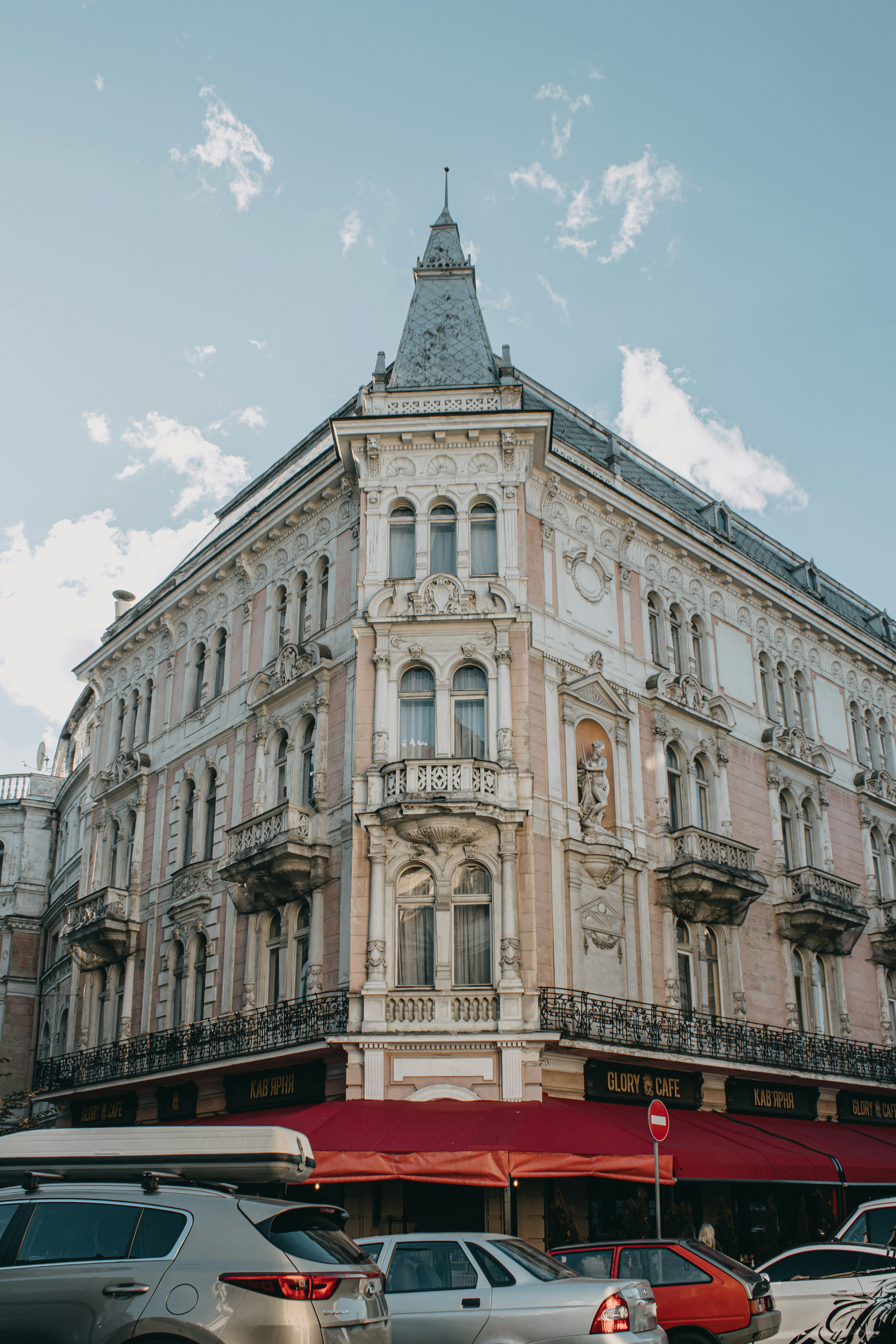 Historic building with ornate architecture and balconies, topped with a pointed spire, set against a bright blue sky.