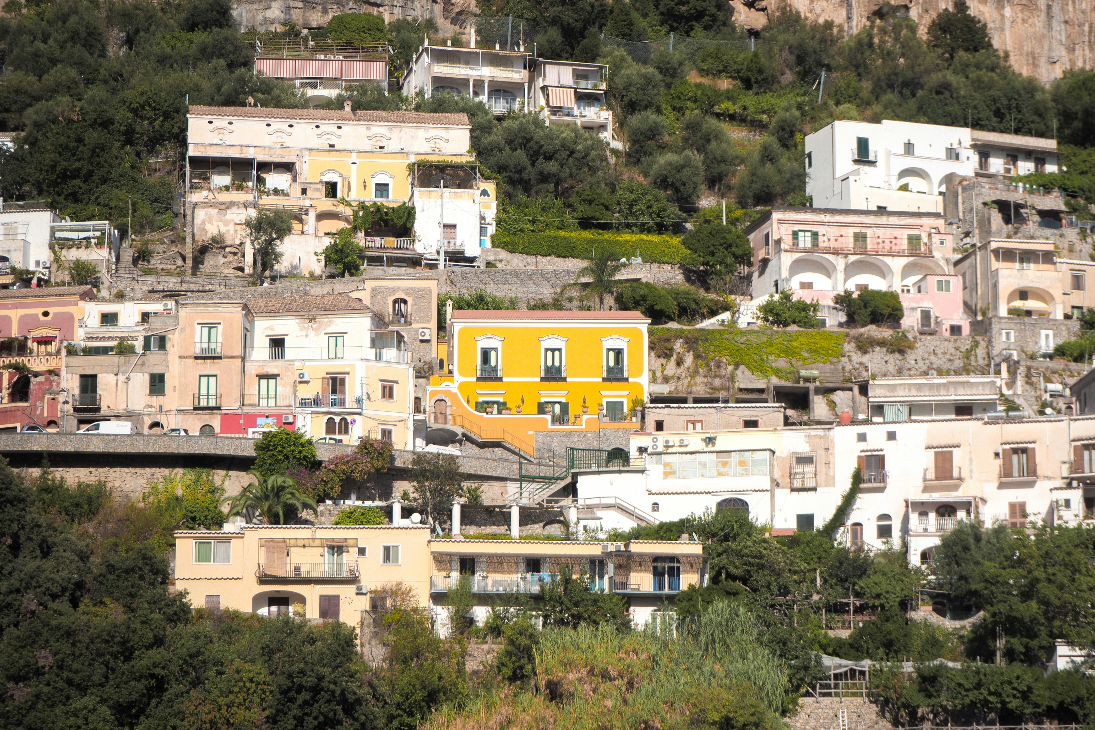Colorful houses nestled on a hillside, showcasing a blend of architectural styles against a lush backdrop. The standout yellow building adds a lively contrast to the scene.