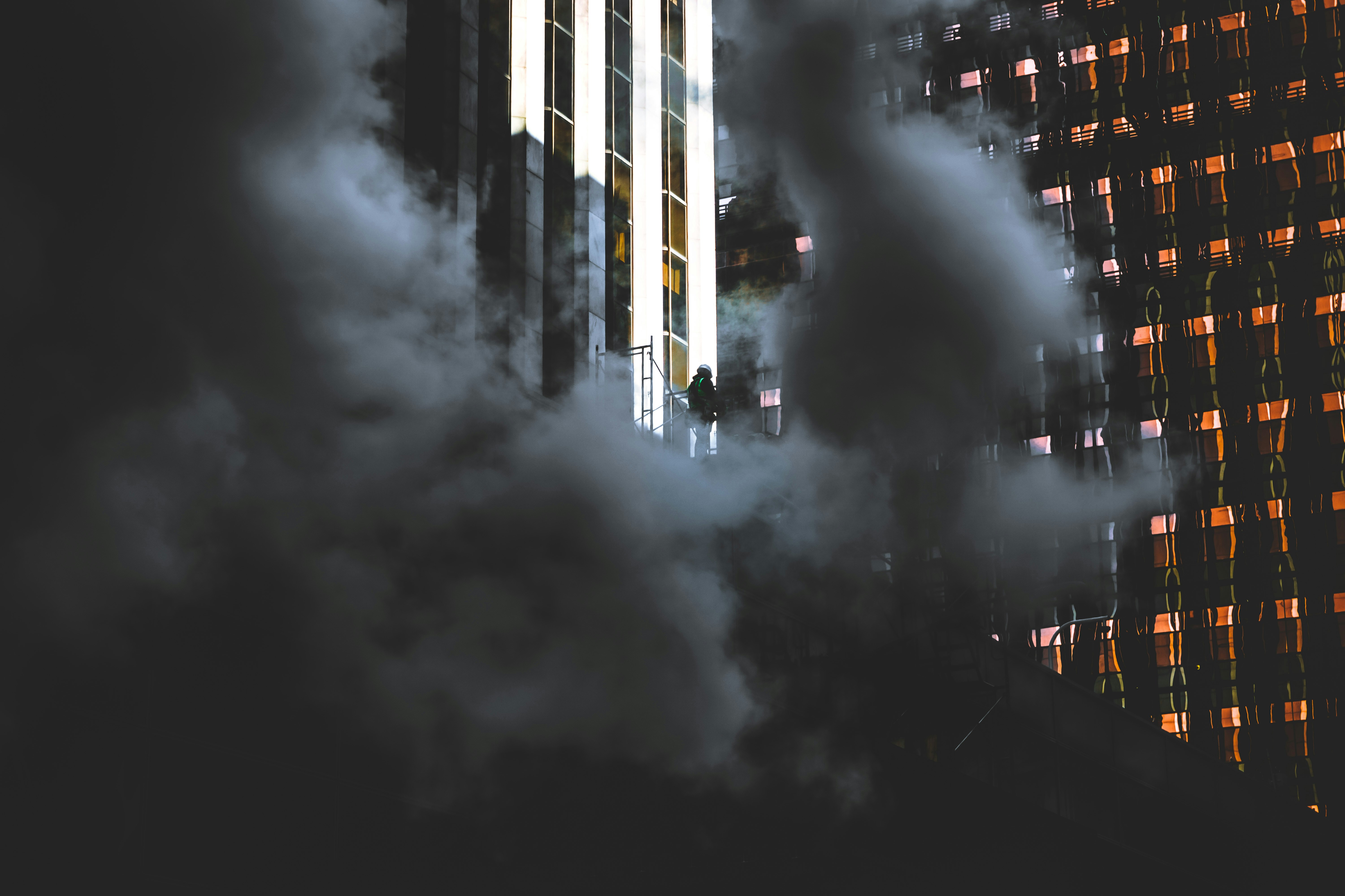 Silhouette of a person amidst steam from a street vent with illuminated buildings in the background.