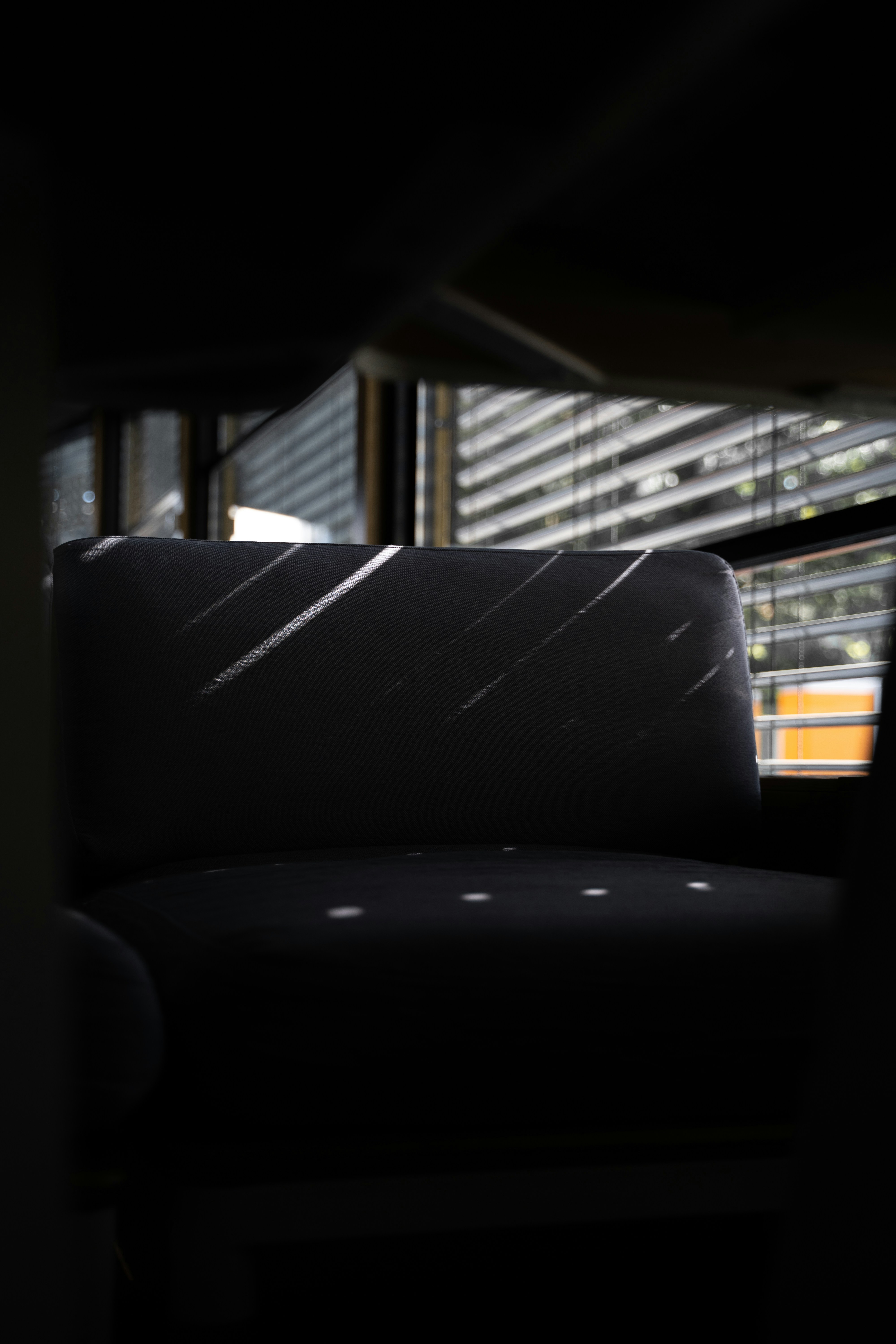 Soft rays of sunlight dance across a dark upholstered chair, casting delicate patterns on its surface. The interplay of shadow and light creates a tranquil atmosphere.