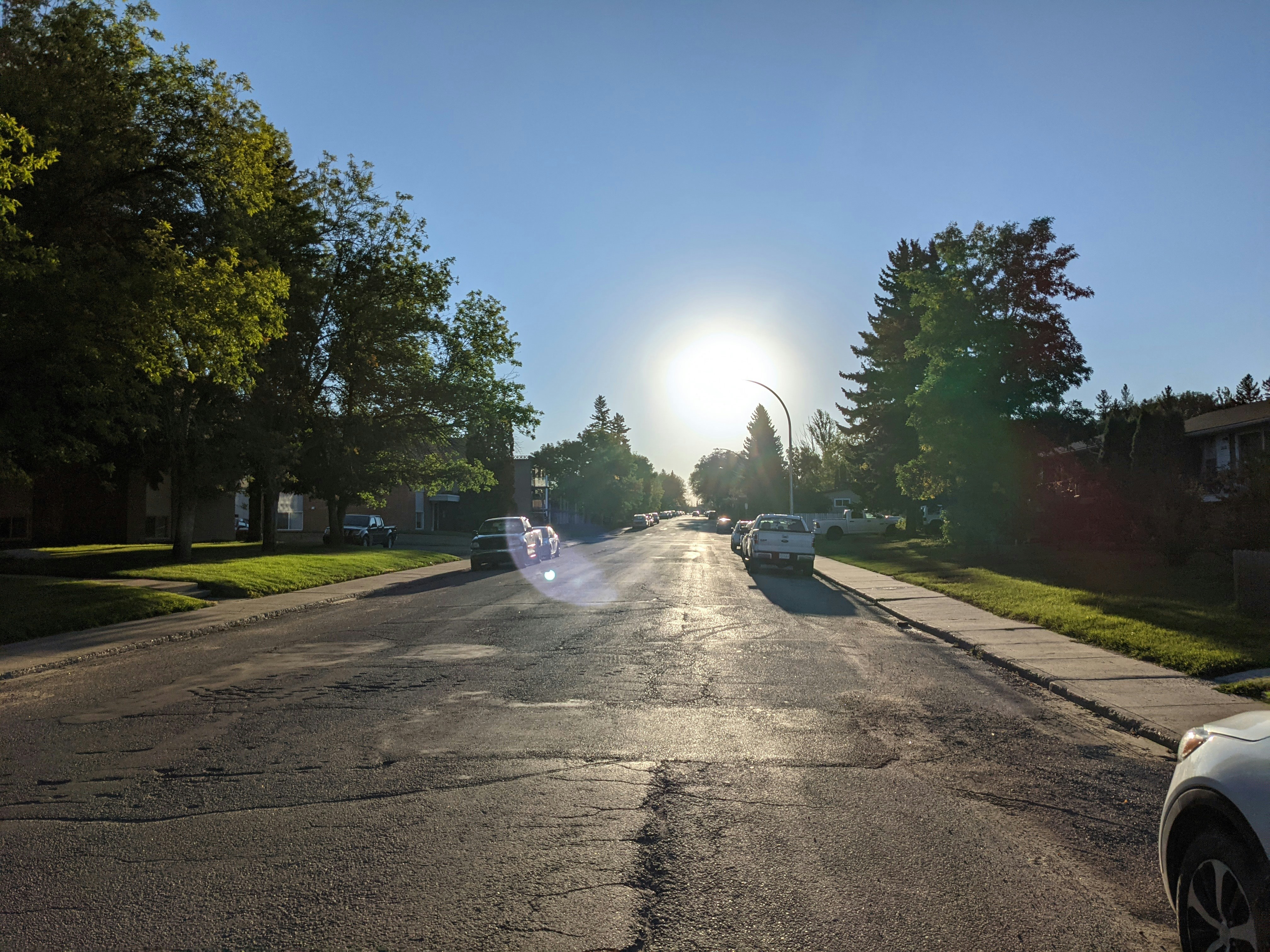 Sunset casting a warm glow over a tranquil residential street lined with trees and parked cars.