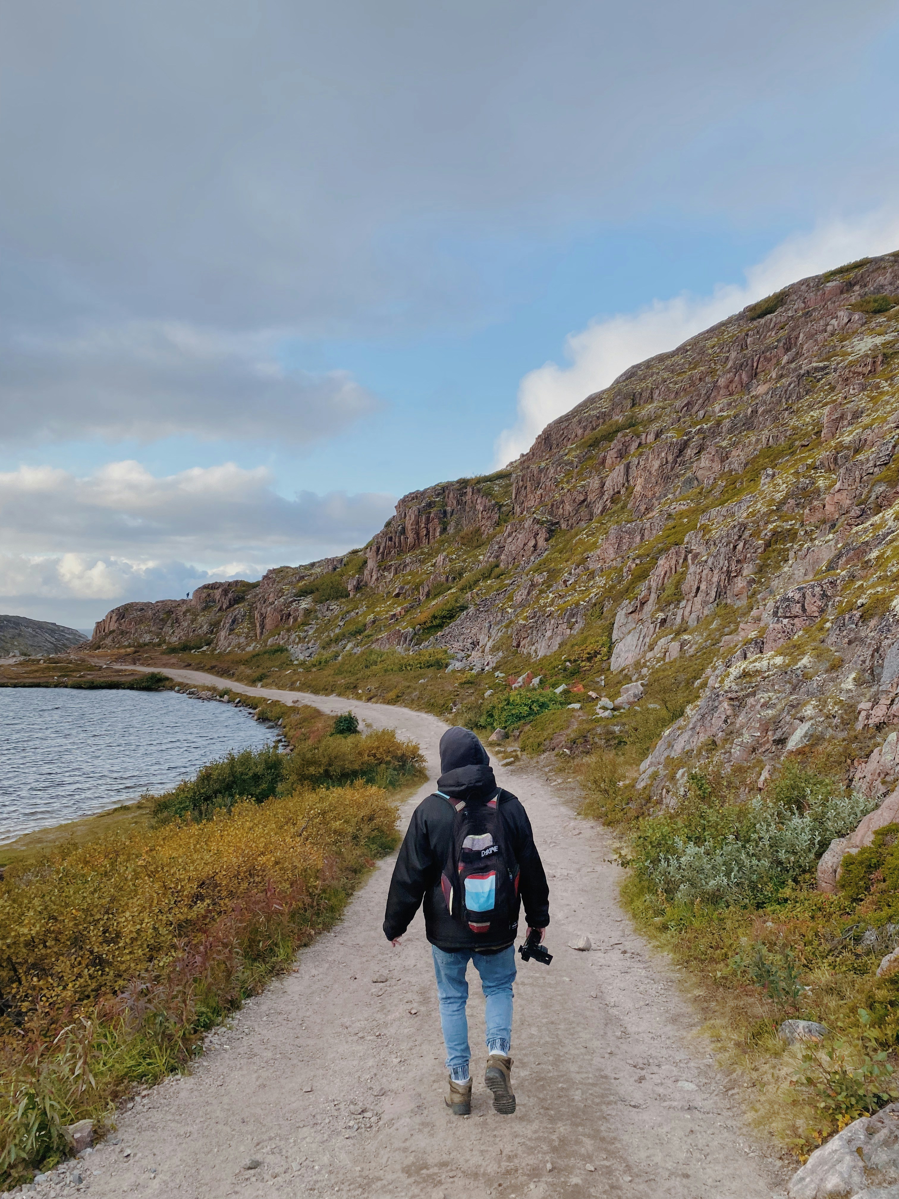 Lone Hiker on a Rocky Coastal Trail Under Cloudy Skies