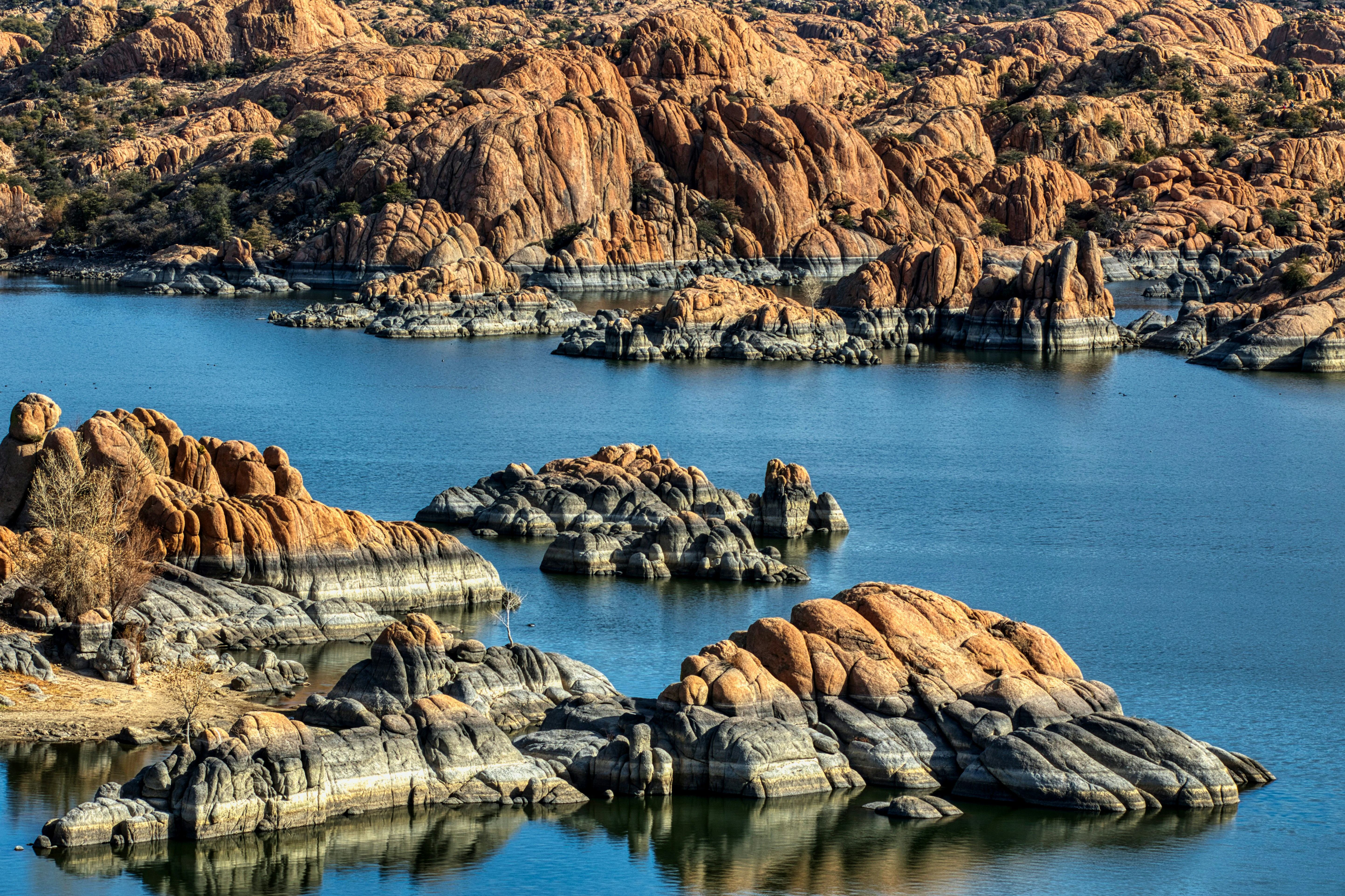 Granite formations jutting out of a tranquil lake, reflecting the surrounding landscape under clear skies.