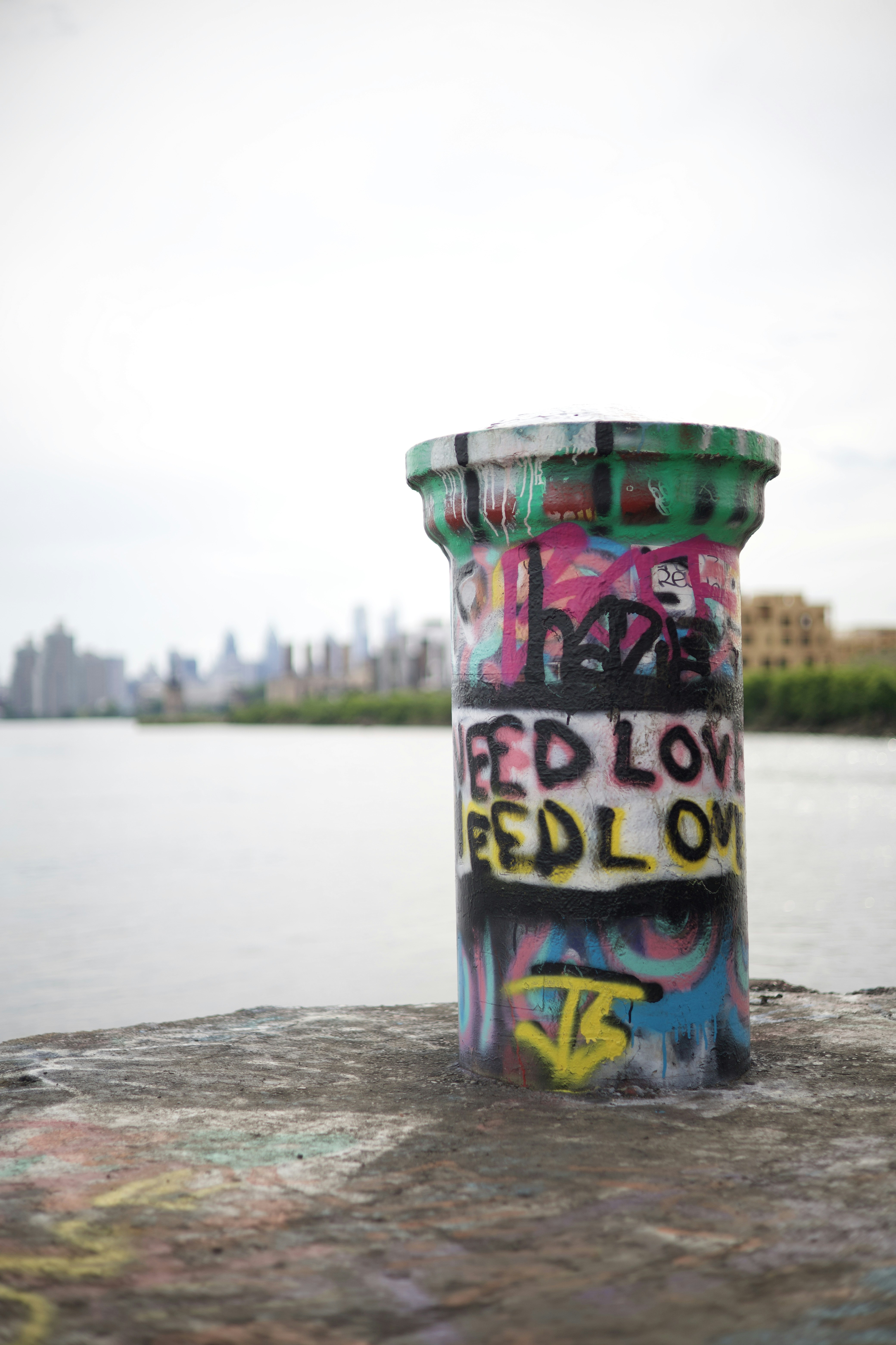Graffiti Column by the River with Urban Skyline in the Distance