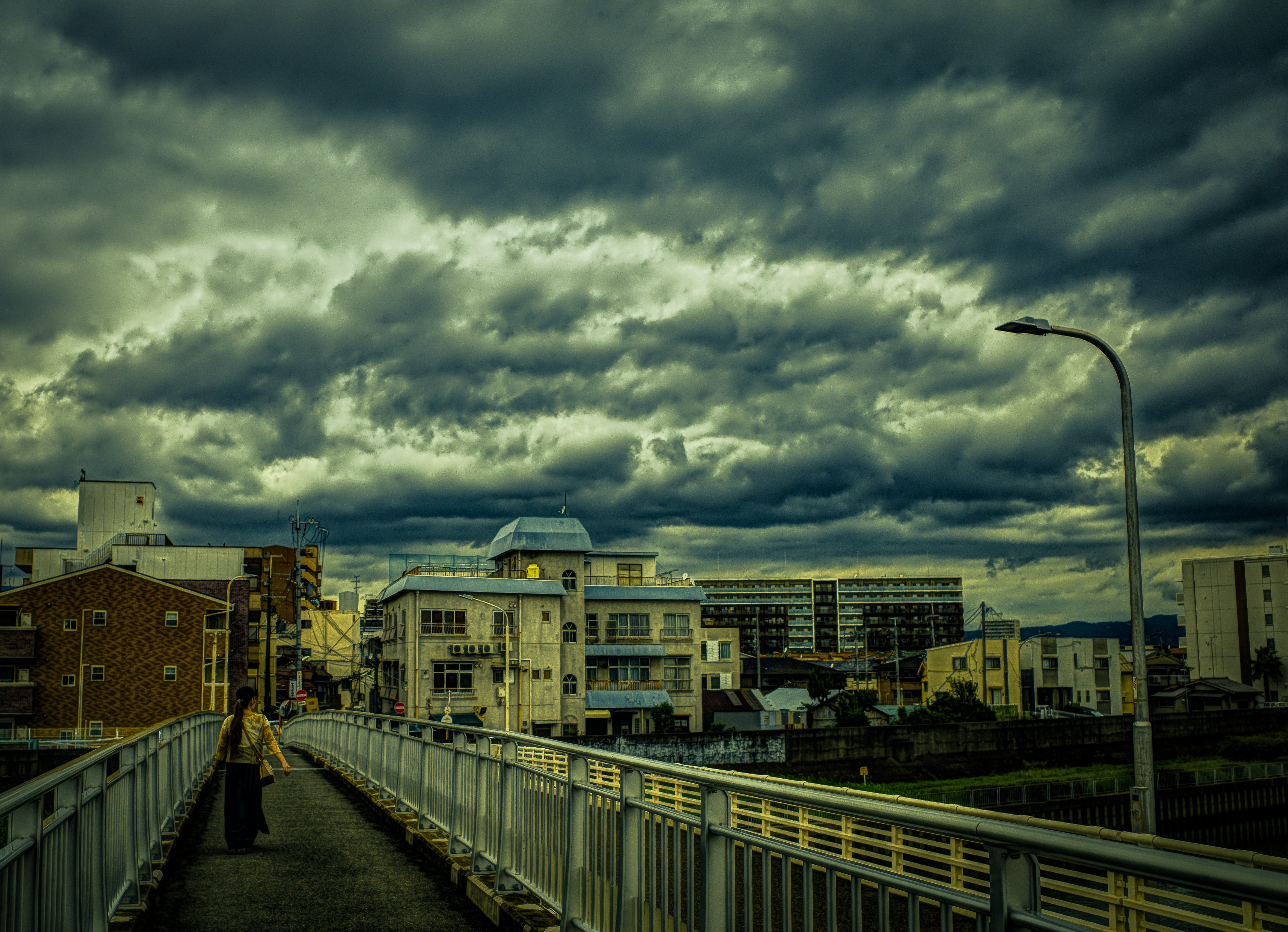 Footpath Toward a Stormy Skyline: Pedestrian on a Bridge Beneath Turbulent Clouds