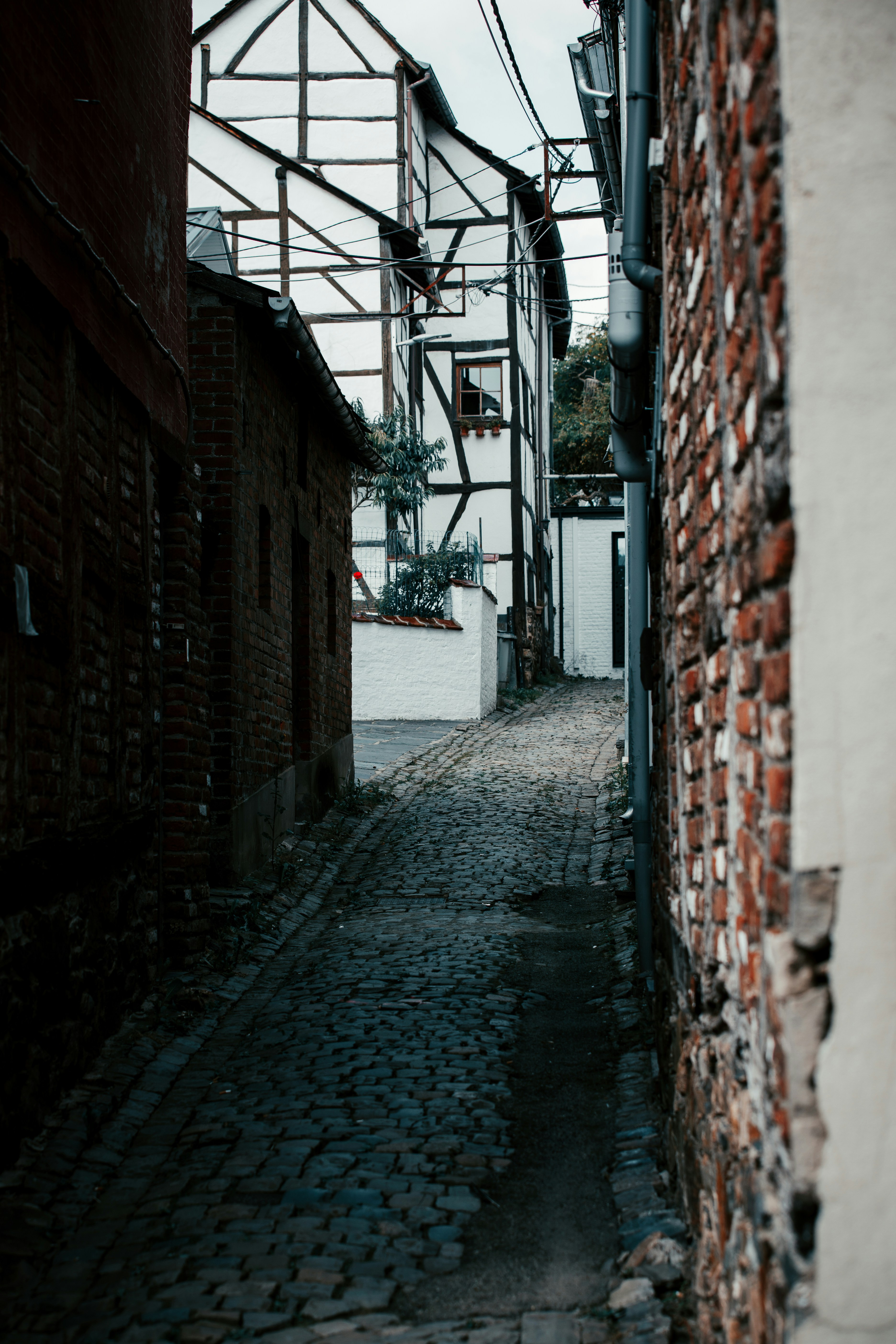 Narrow cobblestone alleyway flanked by rustic buildings, leading to a glimpse of a white structure in the distance.