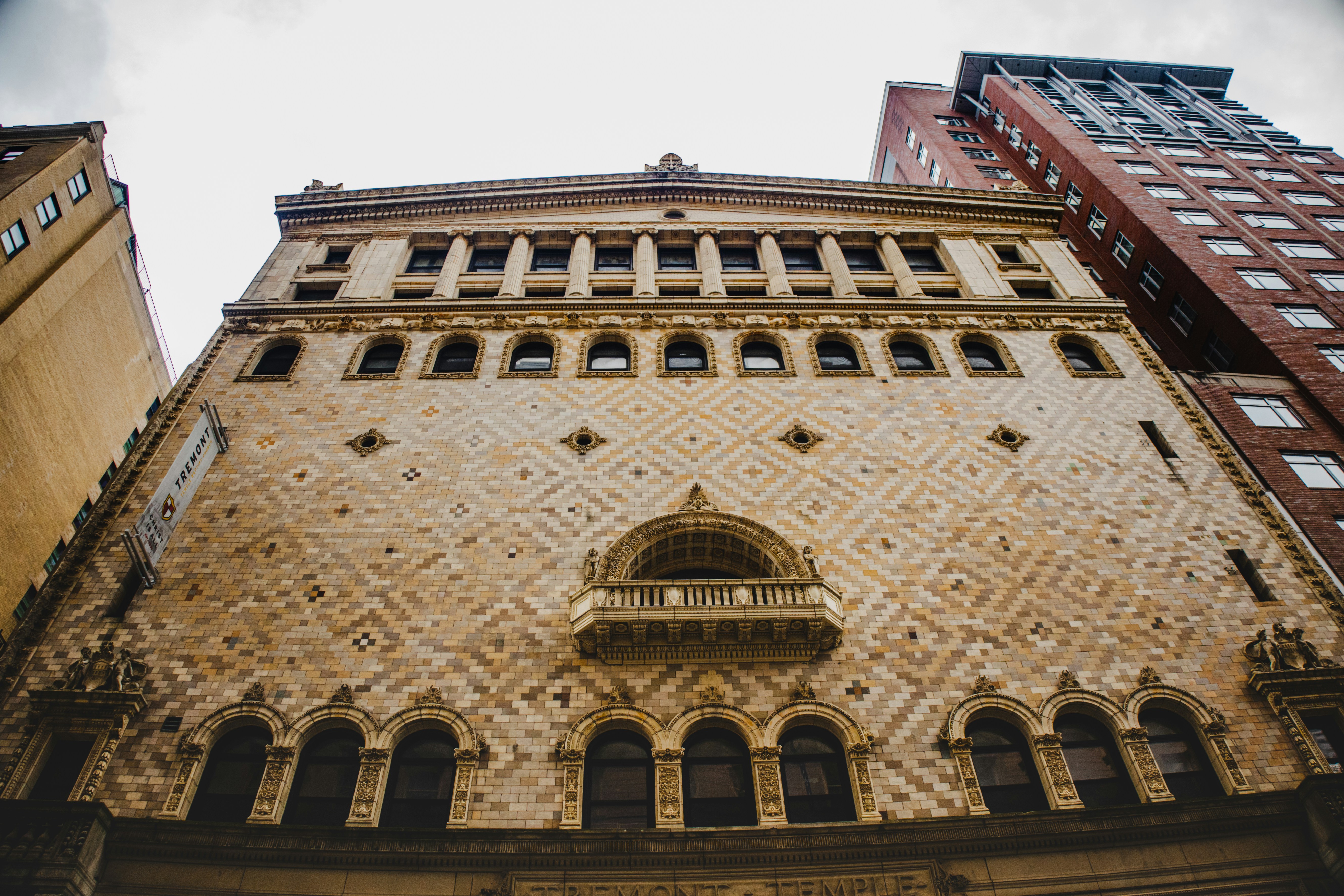 Ornate brown building facade with geometric patterns framed by towering structures under a blue sky.