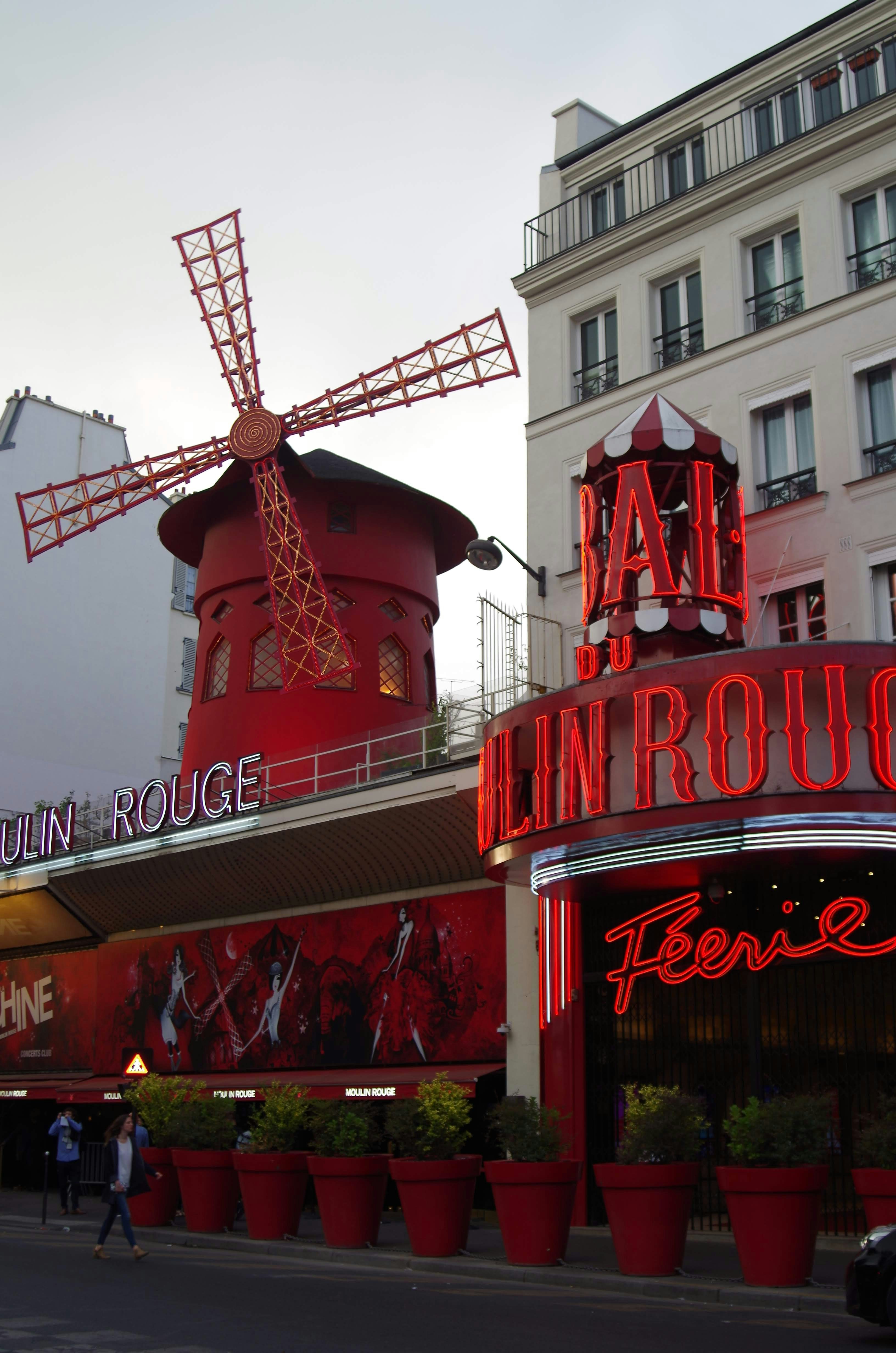 Moulin Rouge's vibrant red windmill and illuminated signage create a lively atmosphere against the evening sky.