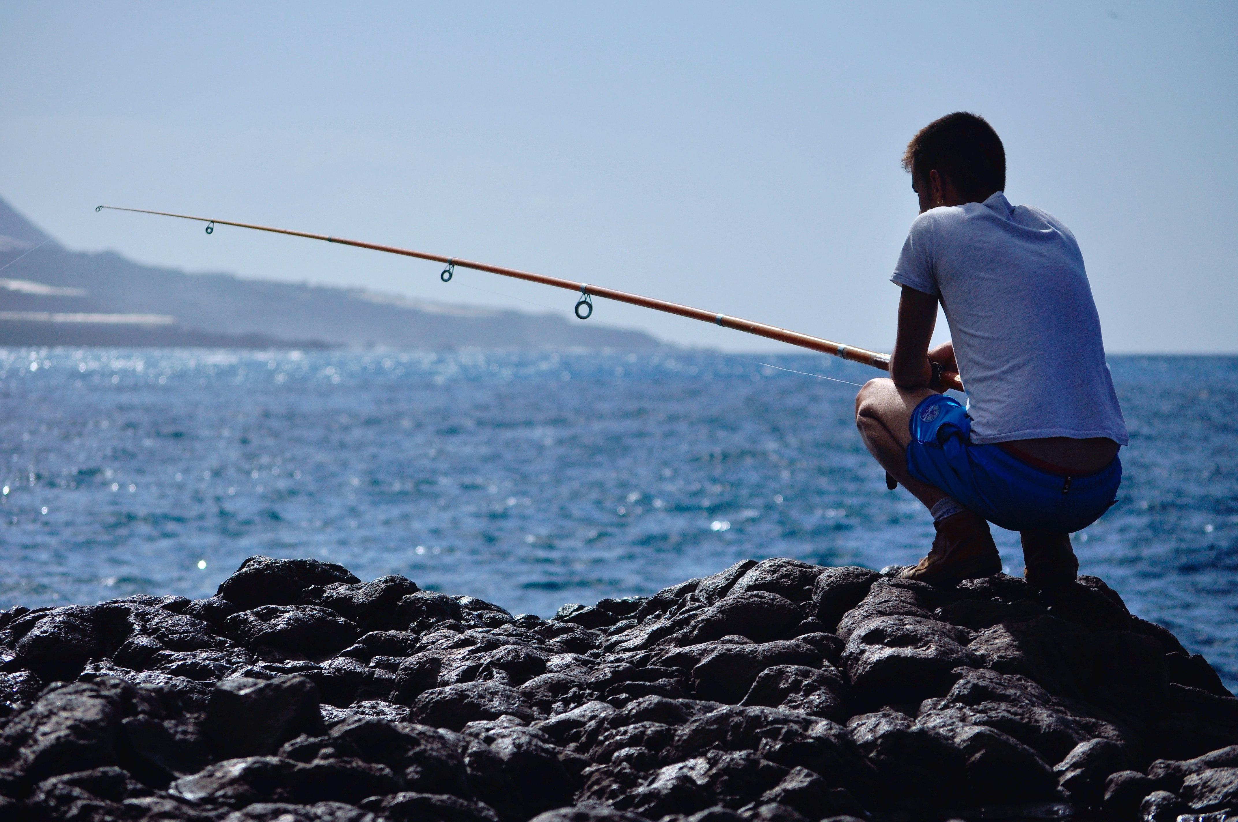 A man sitting on a rock with a fishing rod photo – Free Photo Image on ...