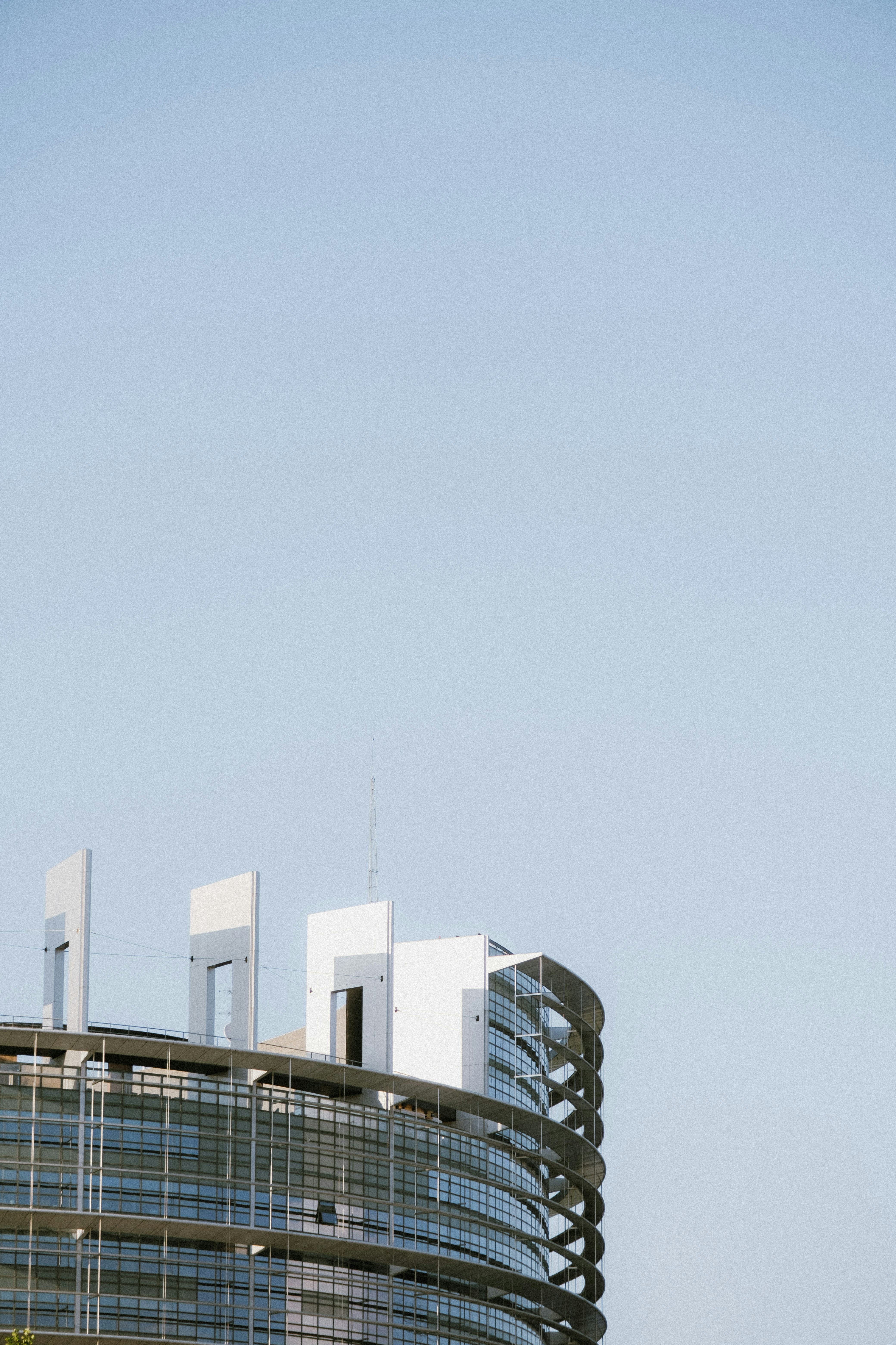 Modern architectural structure with curved glass facade and vertical elements under a clear blue sky.