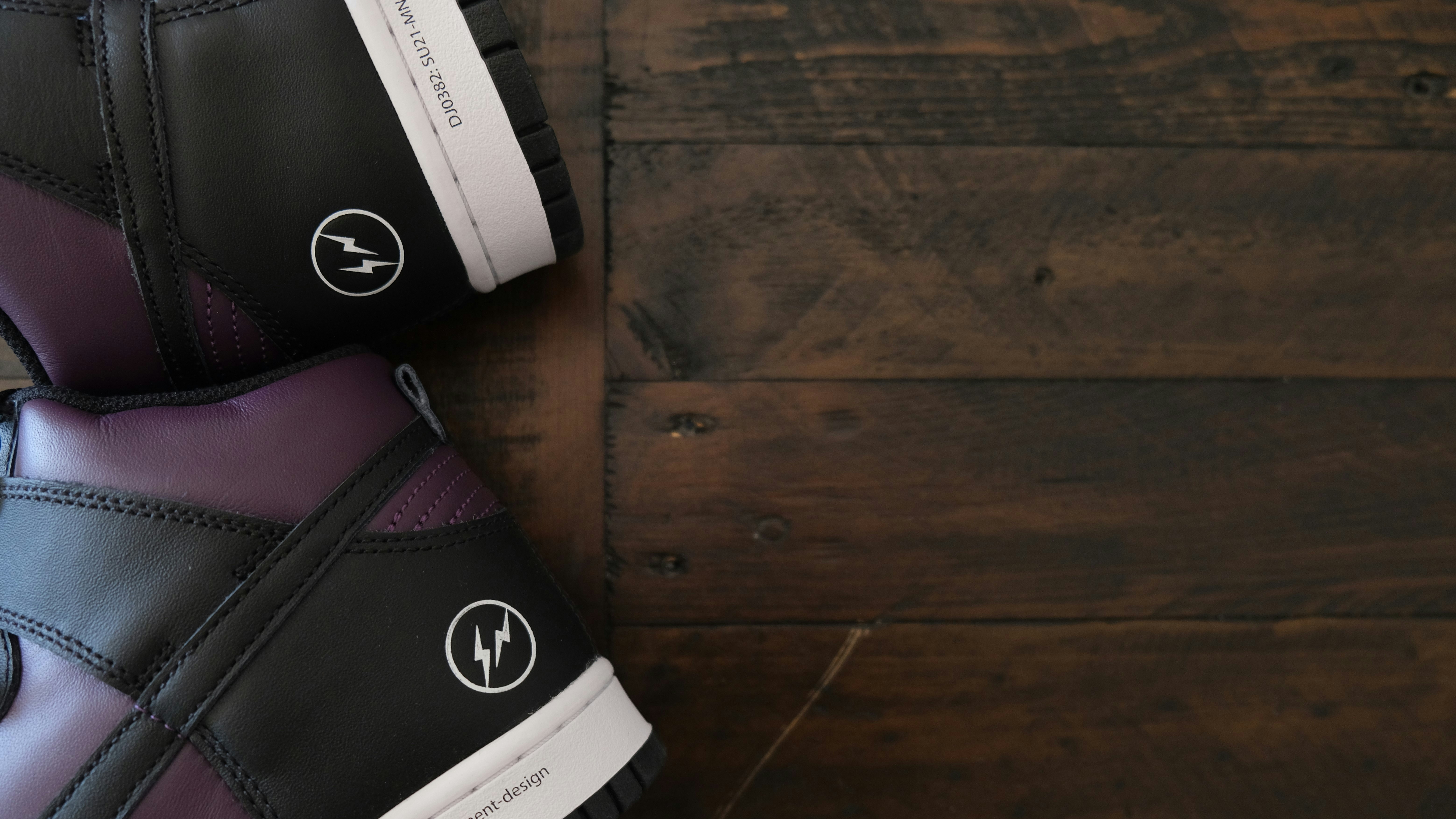 Close-up of stylish black and purple sneakers resting on a wooden surface, showcasing intricate design details and branding.