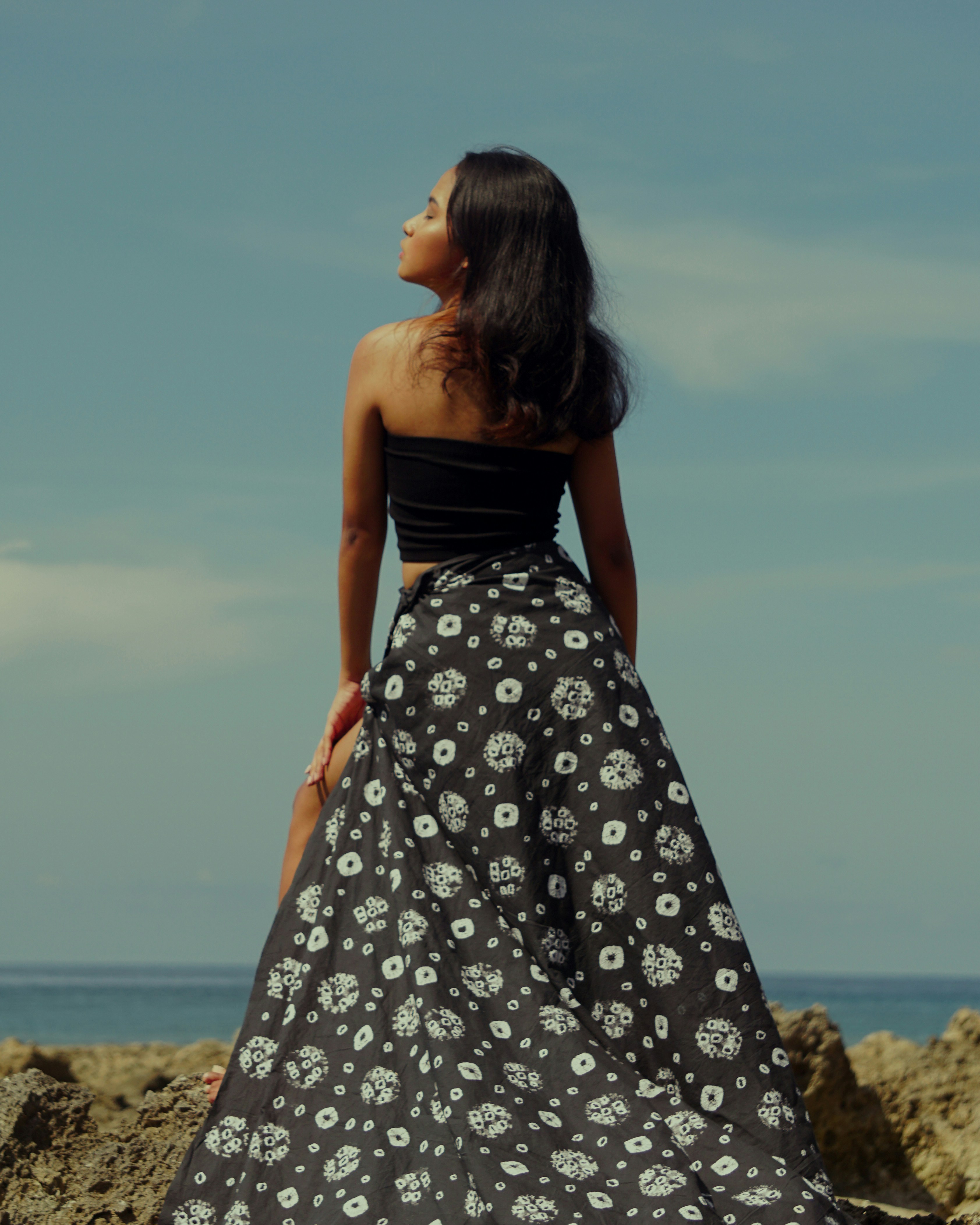 Woman in black and white floral tube dress standing on brown sand ...