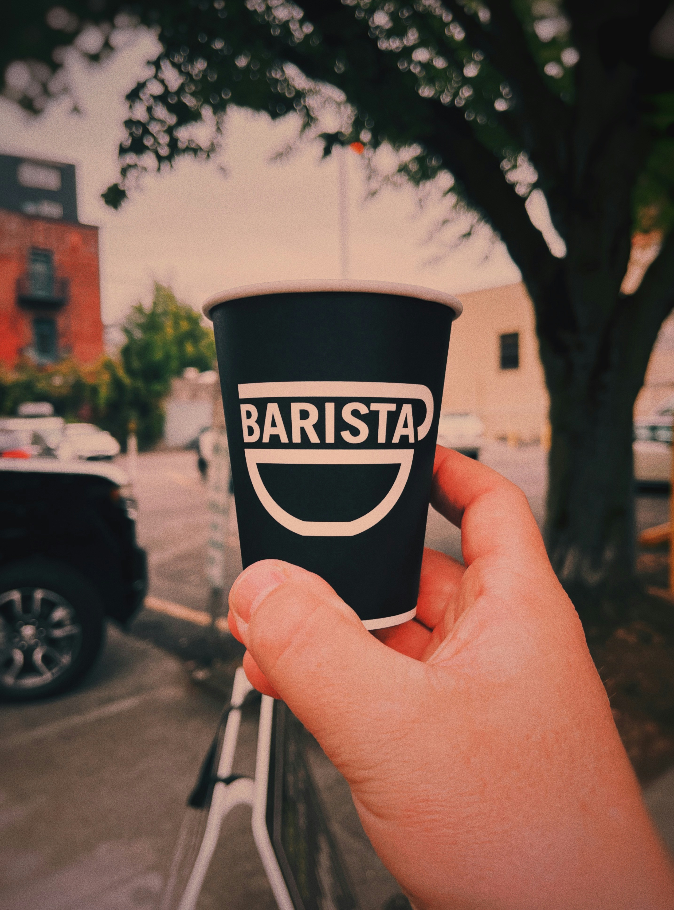 Barista Cup in Focus: A Handheld Moment Against a Blurred Urban Street