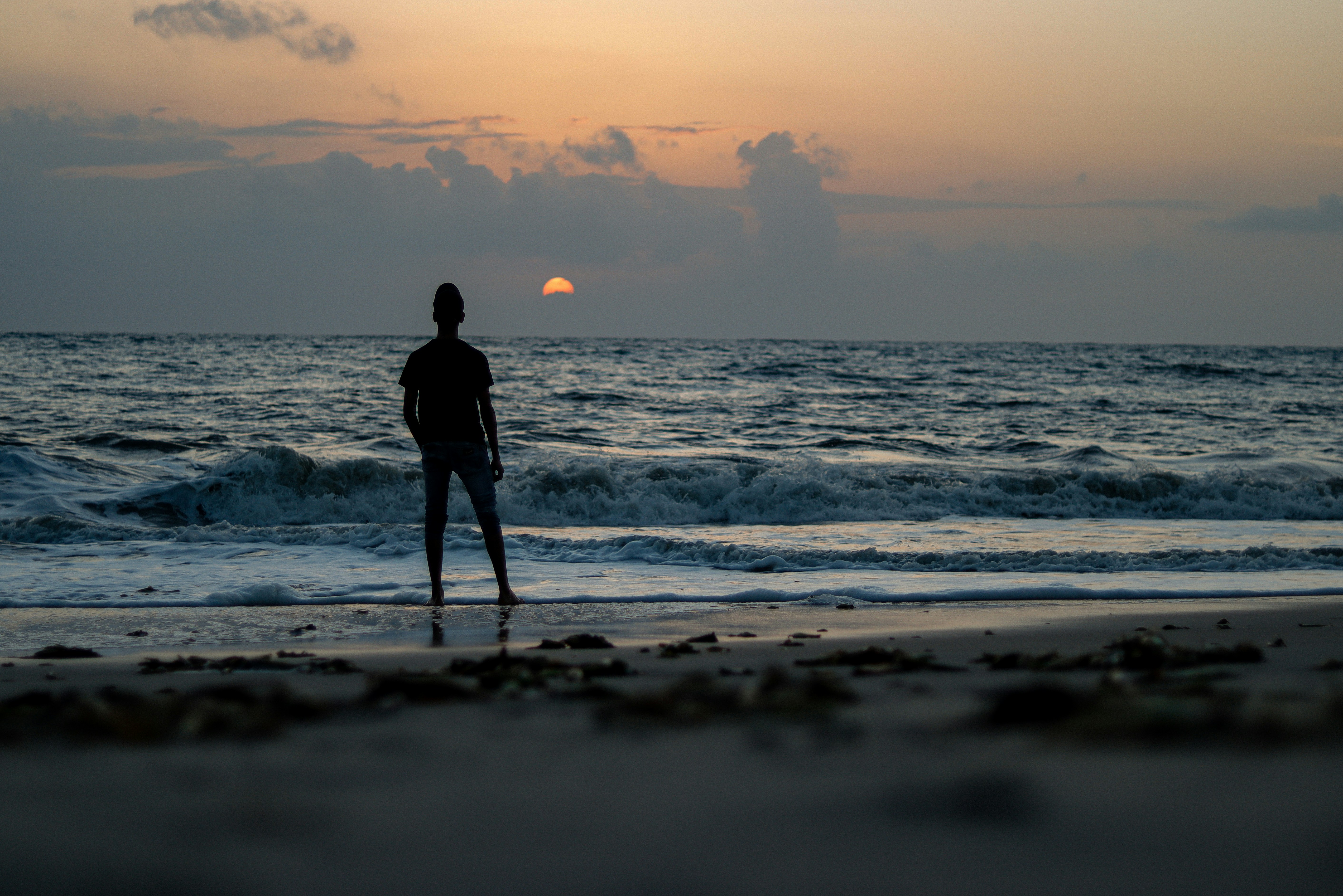 Silhouette of a person standing on a beach watching the sunset over the ocean.