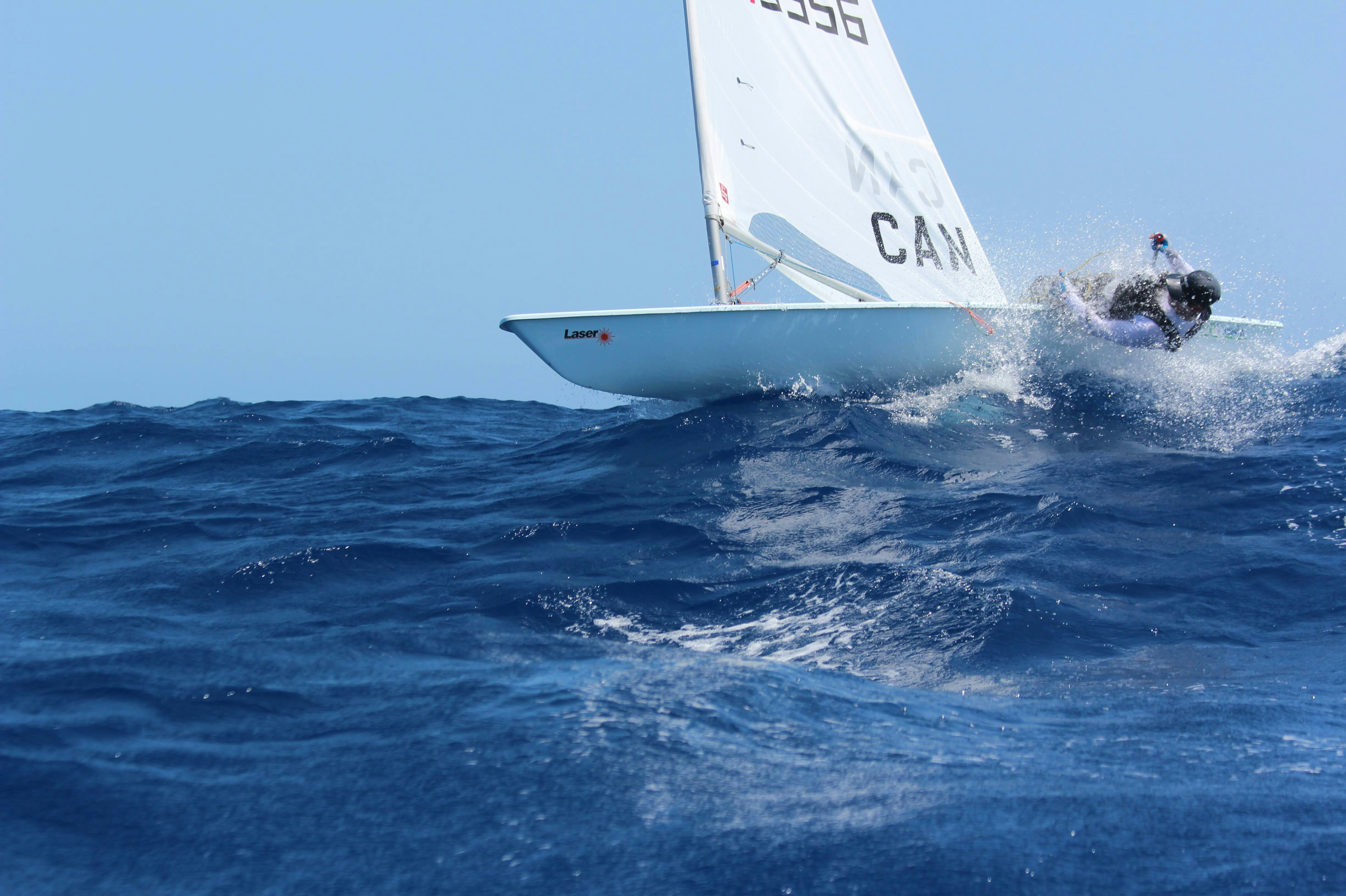 A laser sailboat cuts through vibrant blue ocean waves, showcasing the thrill of sailing. The dynamic motion captures the essence of competitive racing.