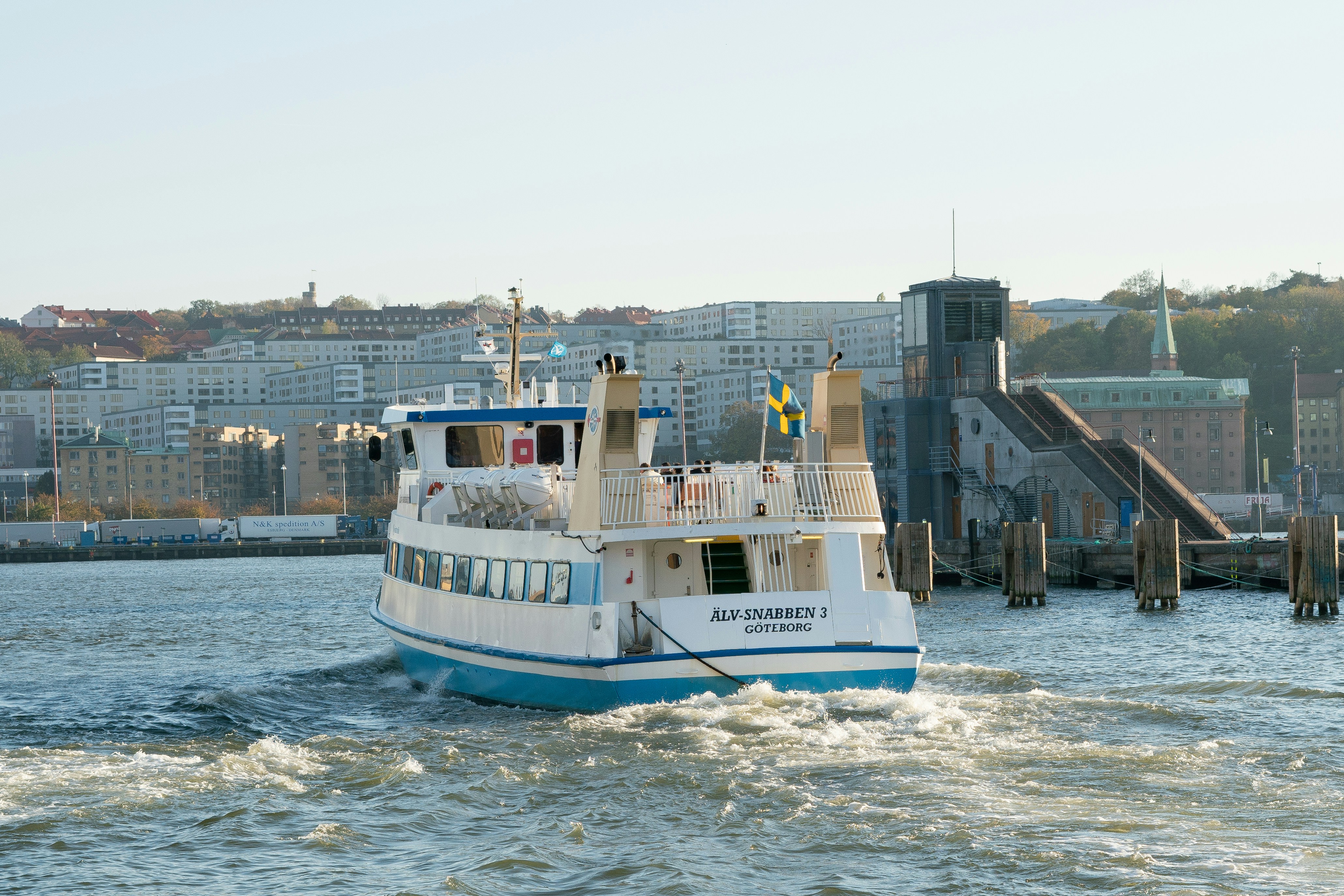 Ferry navigating through a bustling harbor with urban buildings in the background.