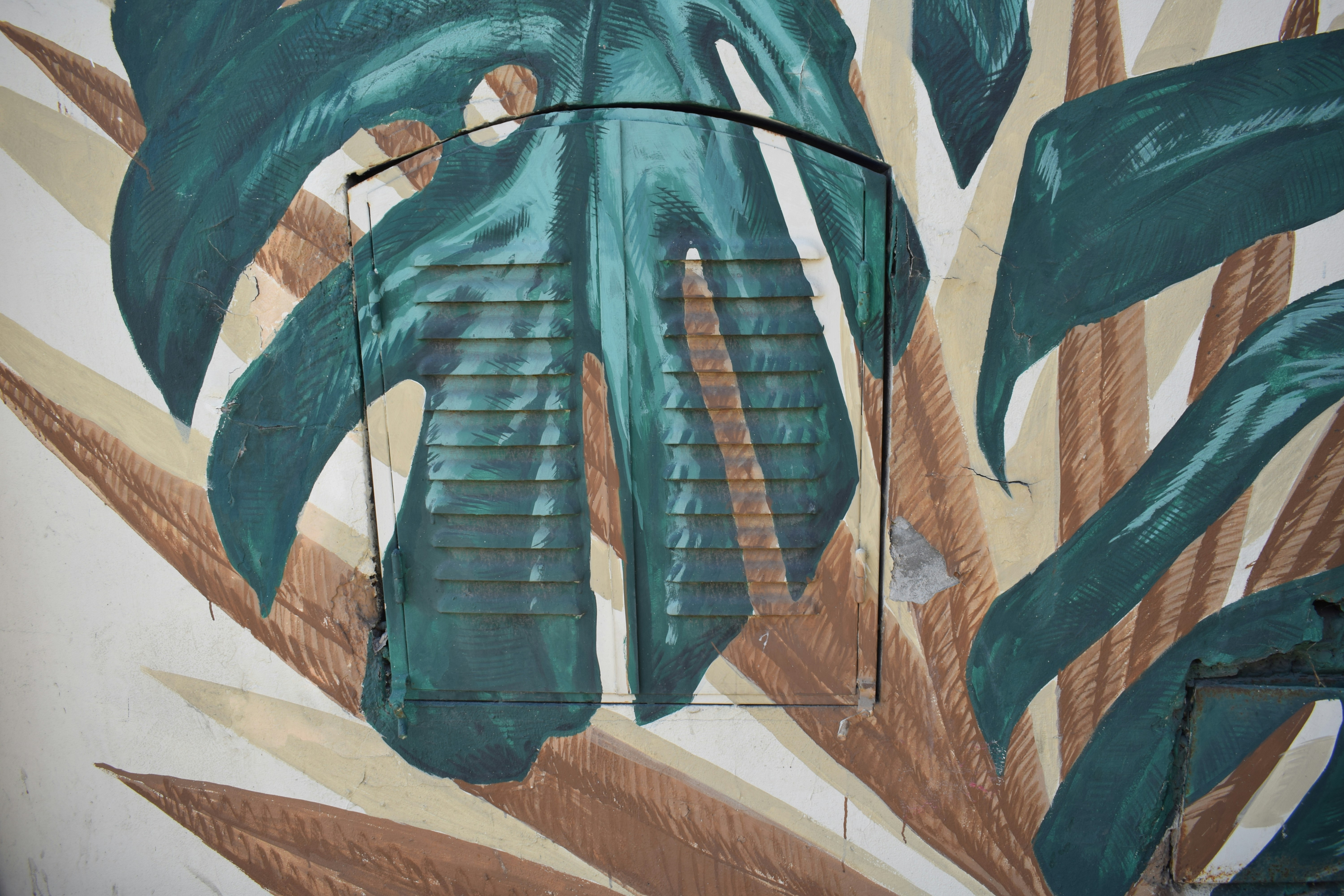 Vibrant mural featuring large green leaves and earthy tones, with a hidden shutter door integrated into the design.