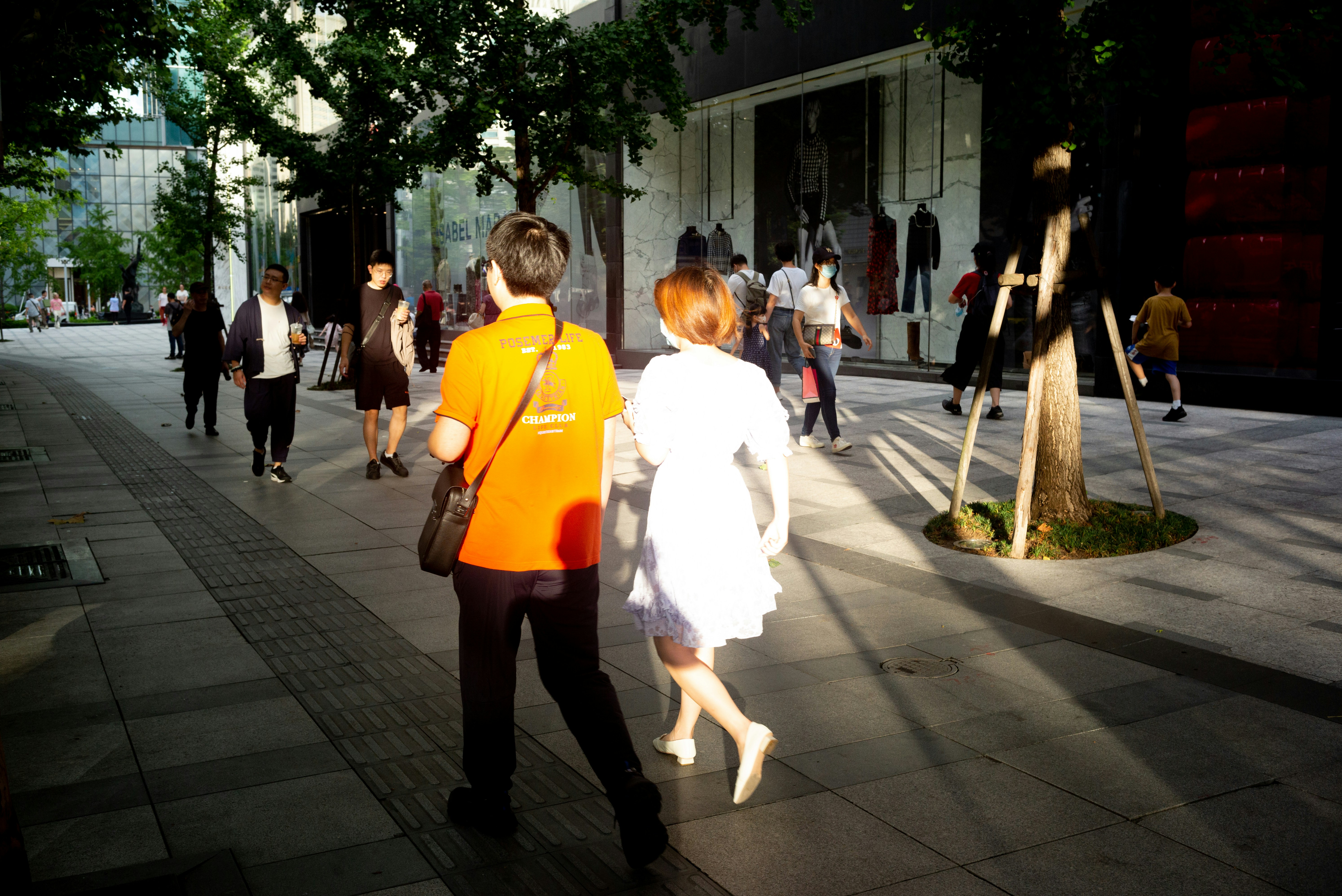 Two figures walk through a bustling city street, illuminated by the warm glow of the setting sun. The scene captures the dynamic energy of urban life.
