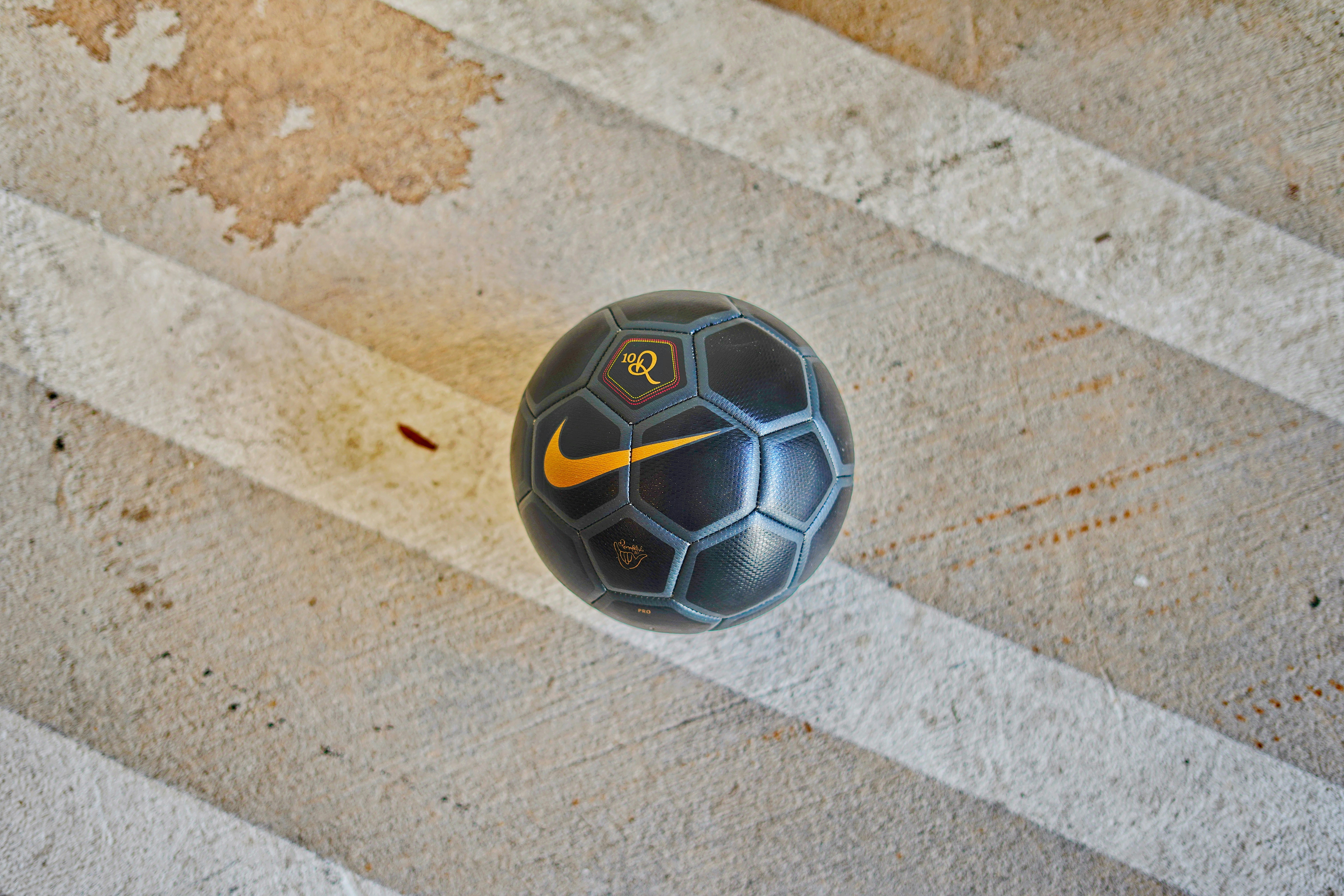 A Nike soccer ball rests on a textured concrete surface, surrounded by white diagonal lines. The scene conveys a sense of anticipation for play.