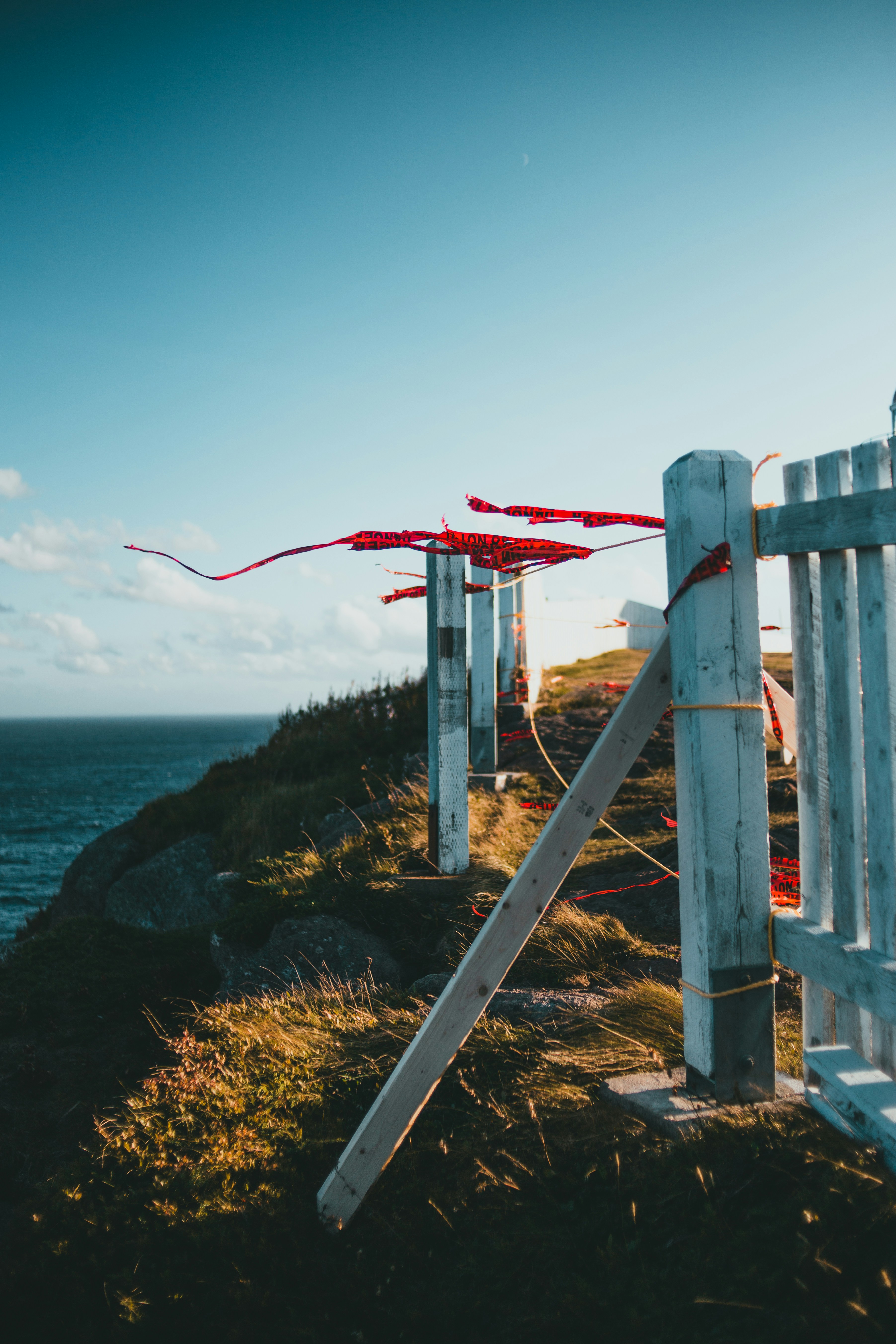 White and red wooden fence on cliff near body of water during daytime ...