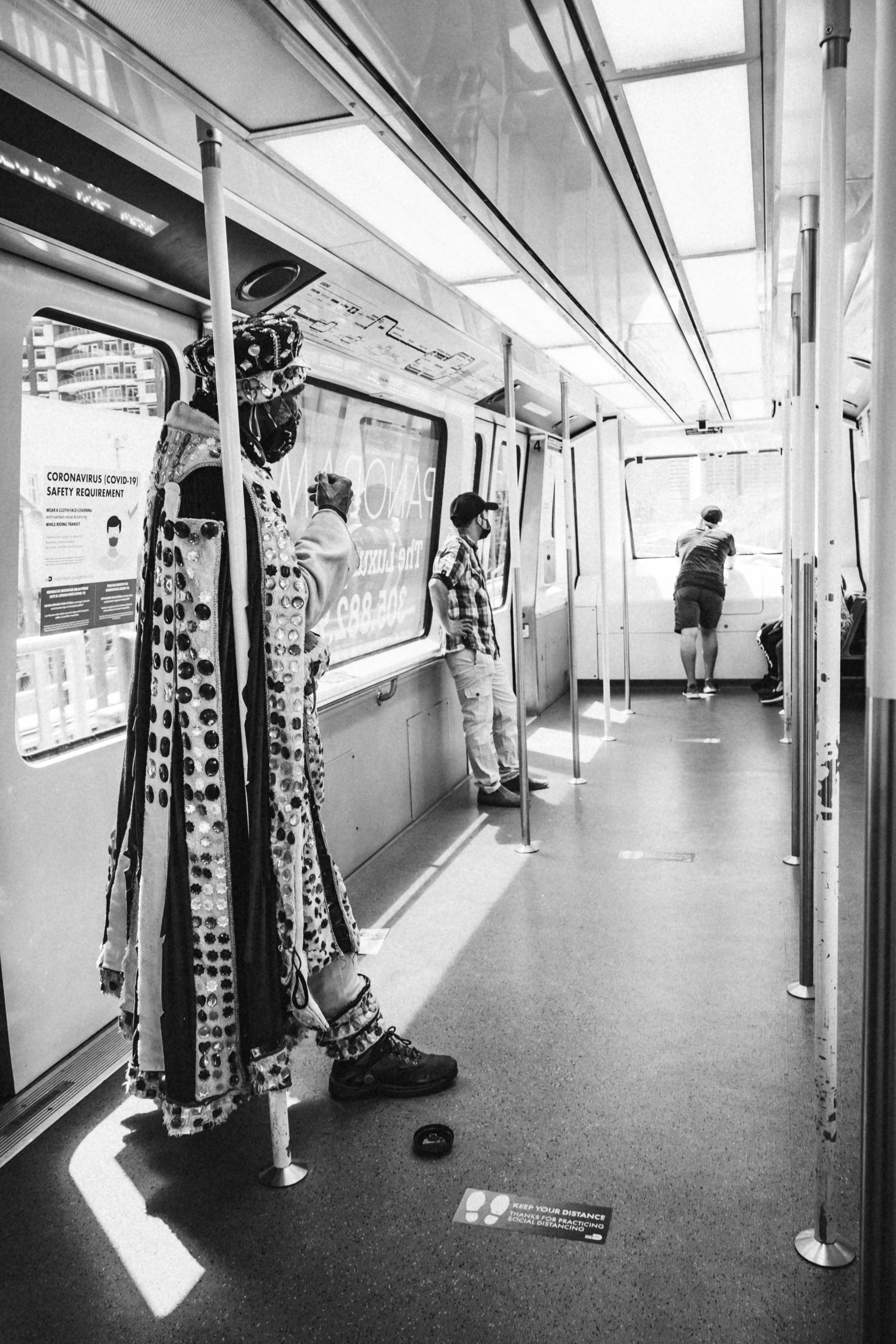 Black-and-white photograph inside a subway car, featuring a lone figure in a long dotted robe standing near the door. The image emphasizes contrast and urban isolation.