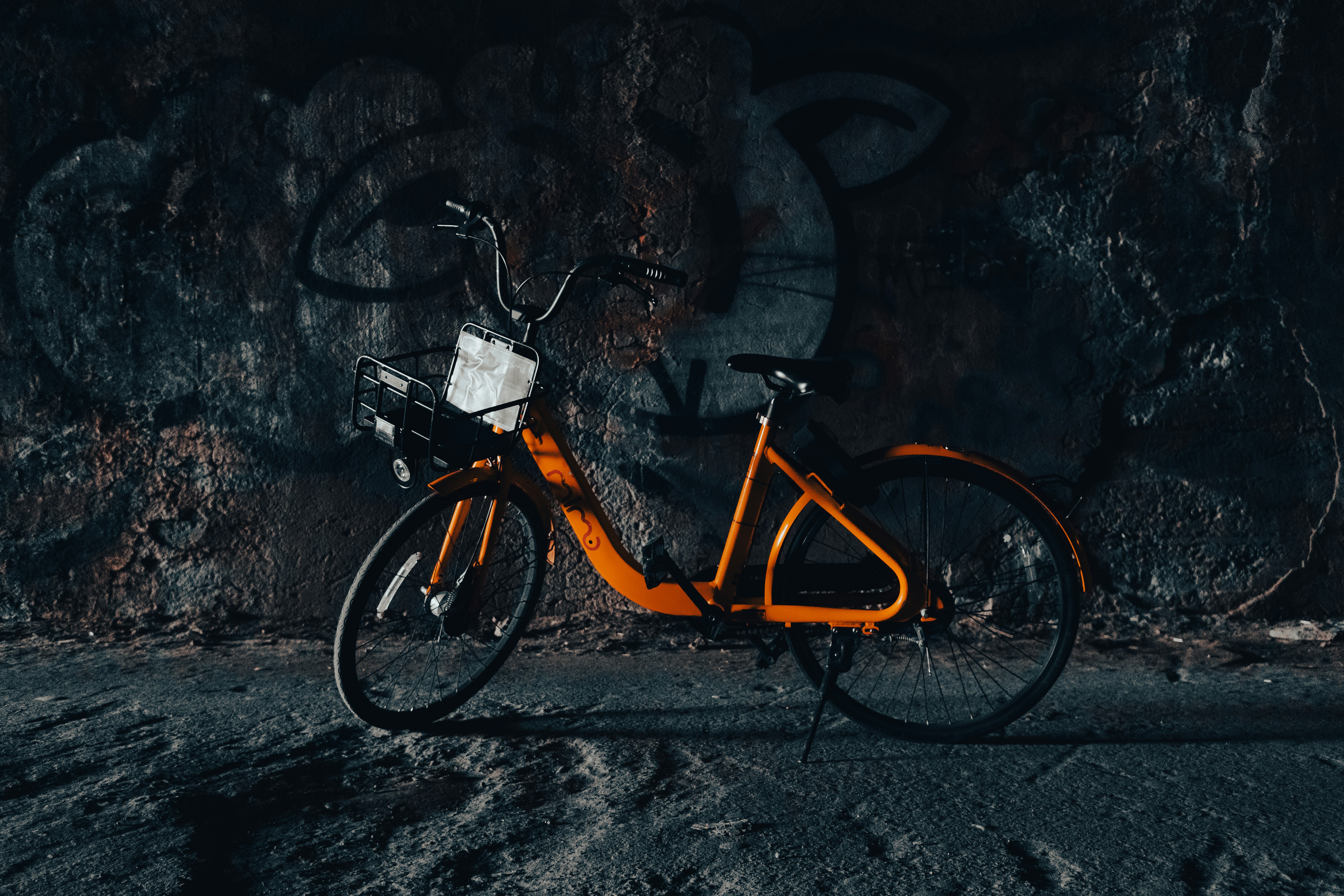 an orange bicycle parked in front of a rock wall