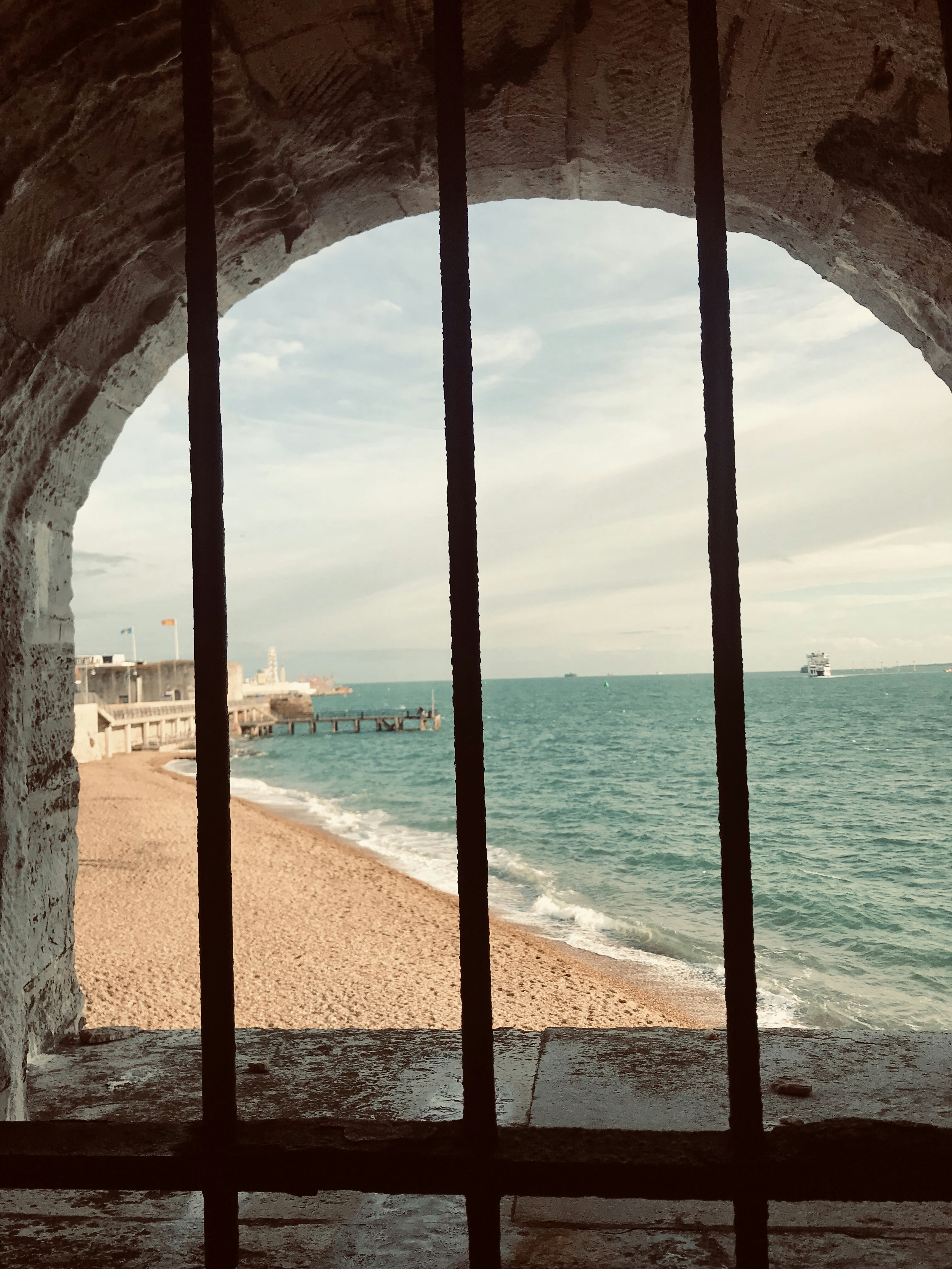 Horizon Through Iron Grilles: A Quiet Shore Framed by Stone