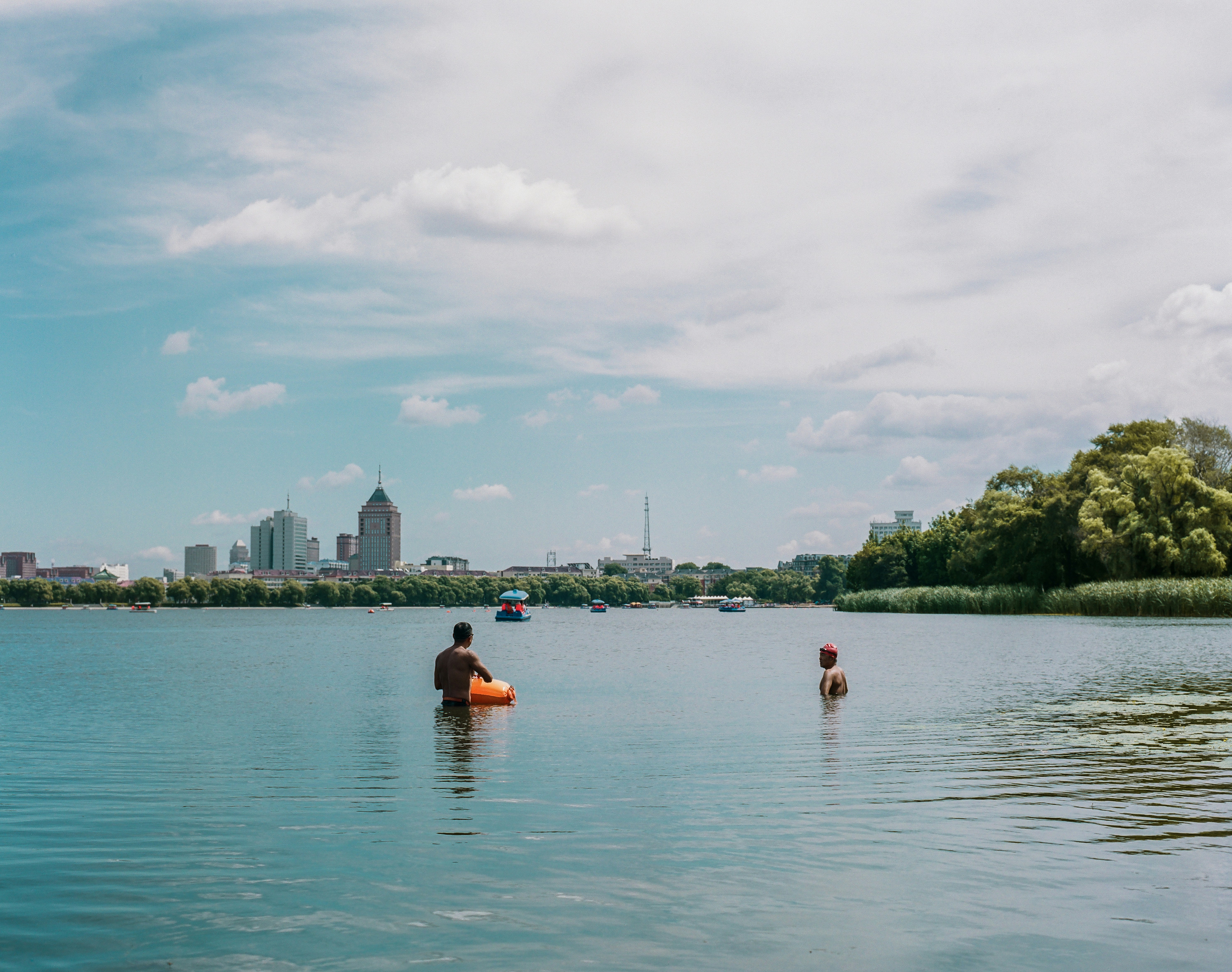 Foto zum Thema Zwei Menschen waten in einem See mit einer Stadt im ...