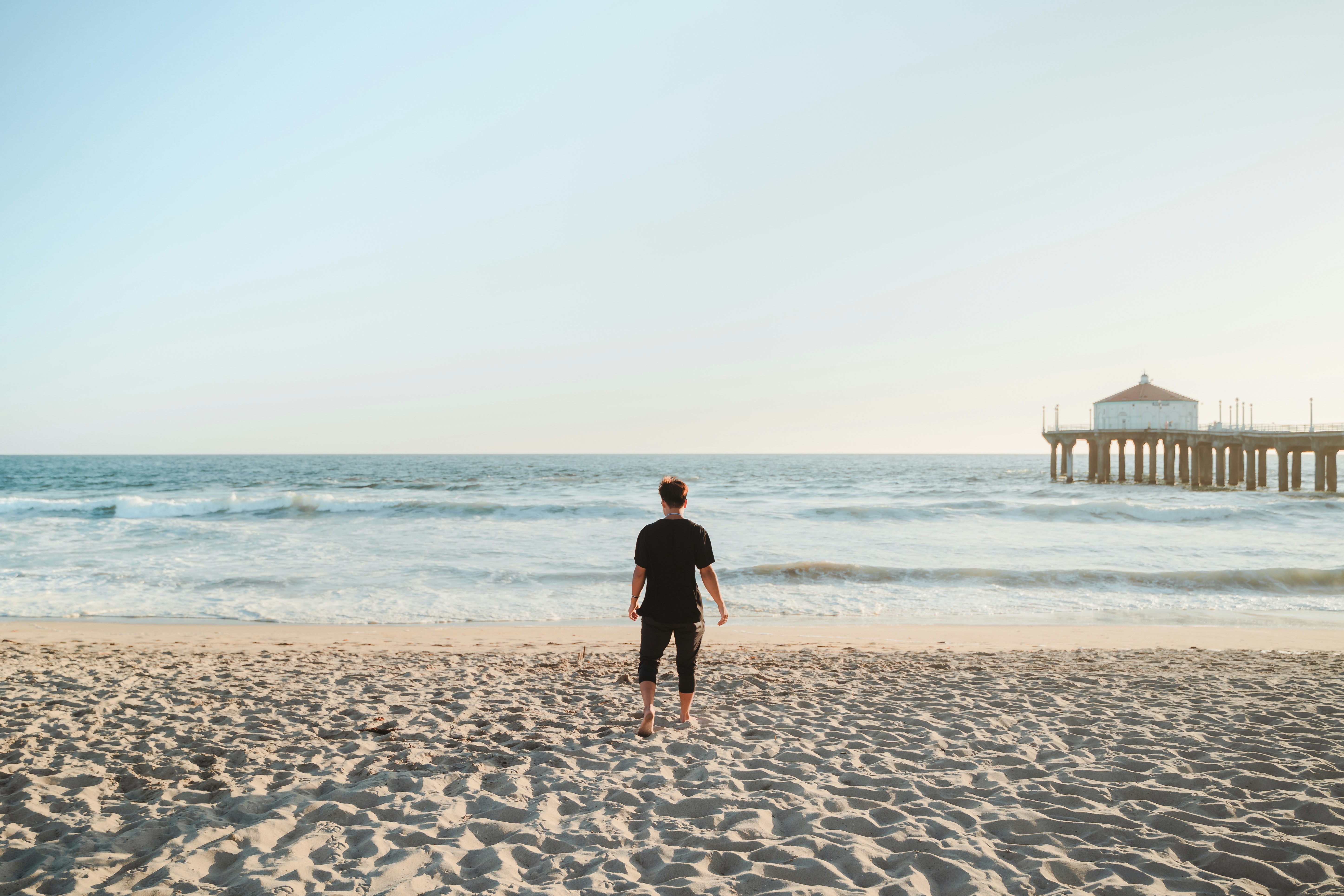 Lone Figure on a Sunlit Shore, Eyeing the Distant Pier