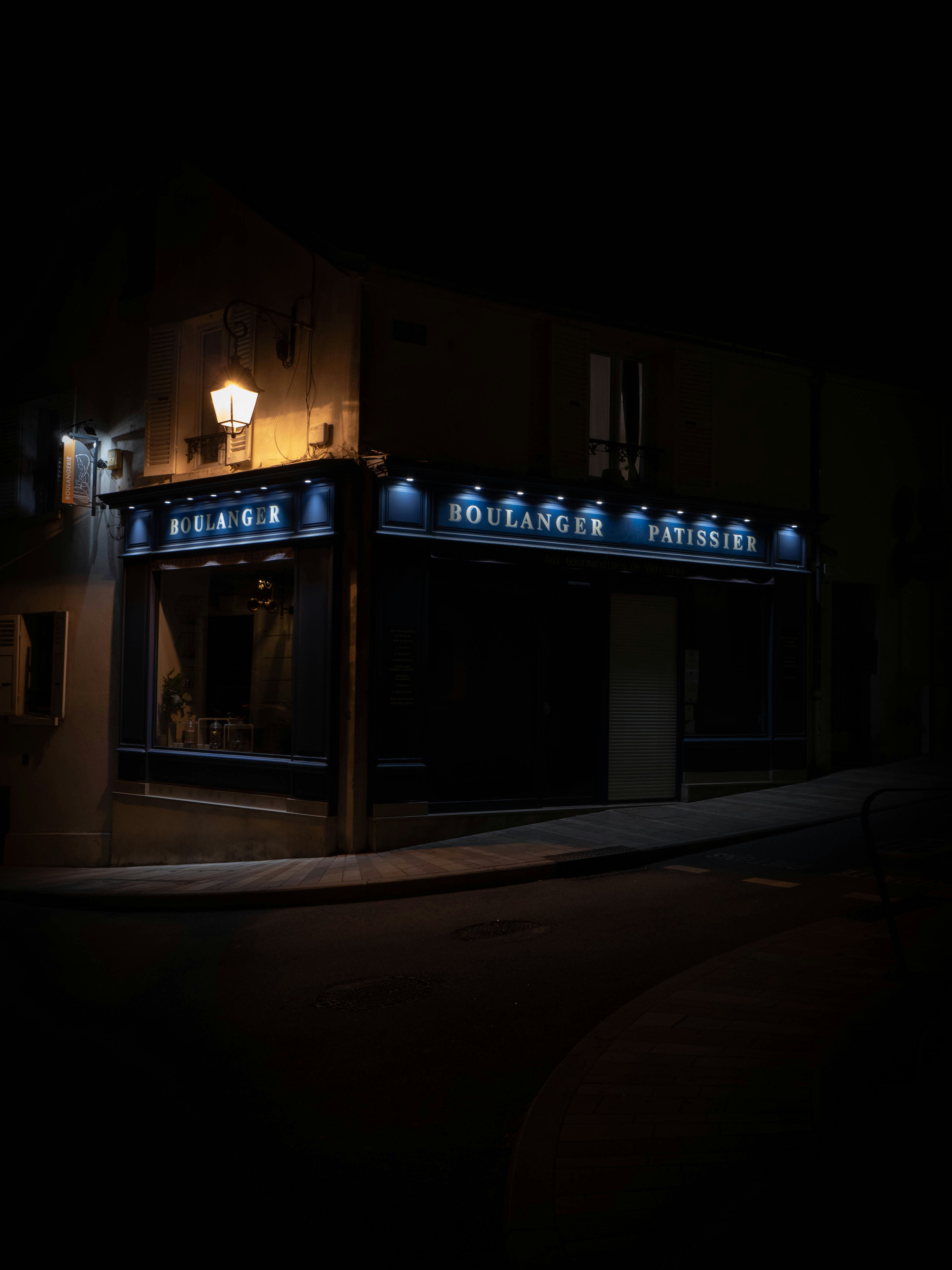 Charming boulangerie and patisserie illuminated by soft streetlights, set against a dark night backdrop.