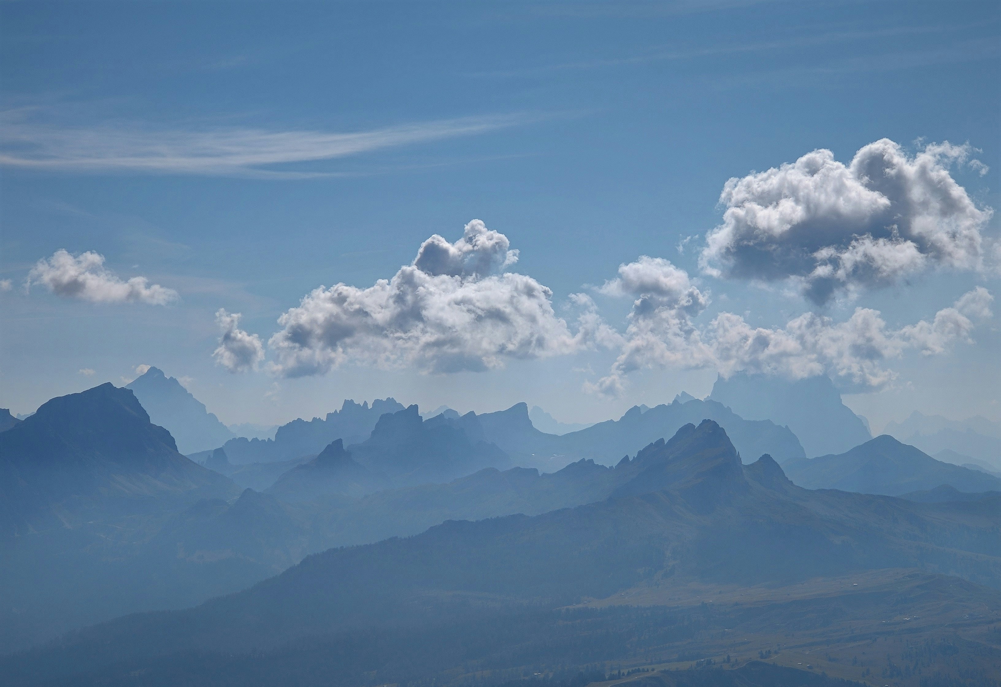 Rolling mountain landscape with scattered clouds against a blue sky.