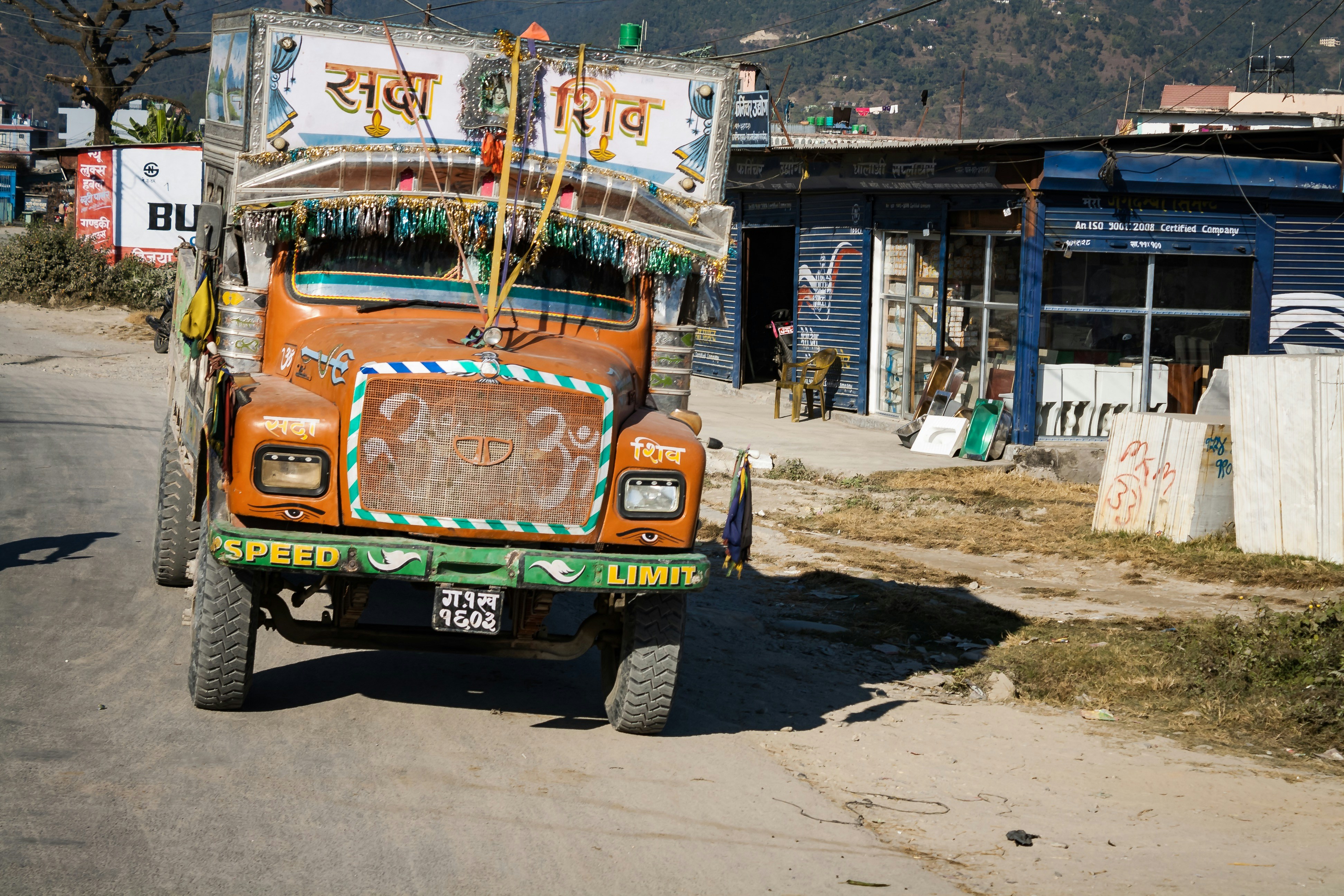 Colorfully decorated truck navigating a rural road, showcasing intricate artwork and cultural elements. The scene reflects the unique transportation aesthetics of India.