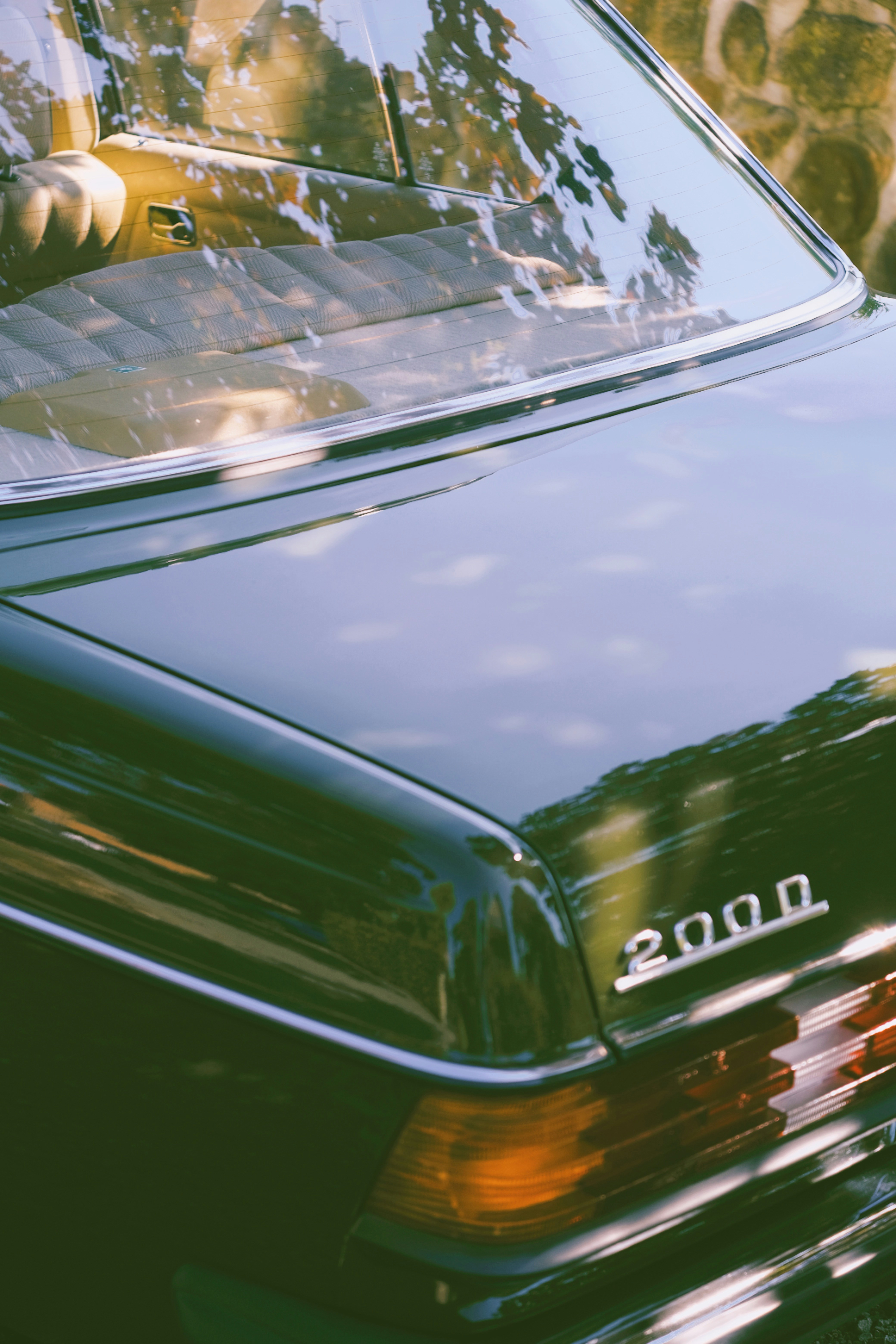 Close-up of a vintage car's rear, showcasing its sleek lines and the iconic '2000' badge. Sunlight reflects off the polished surface, adding a nostalgic feel.