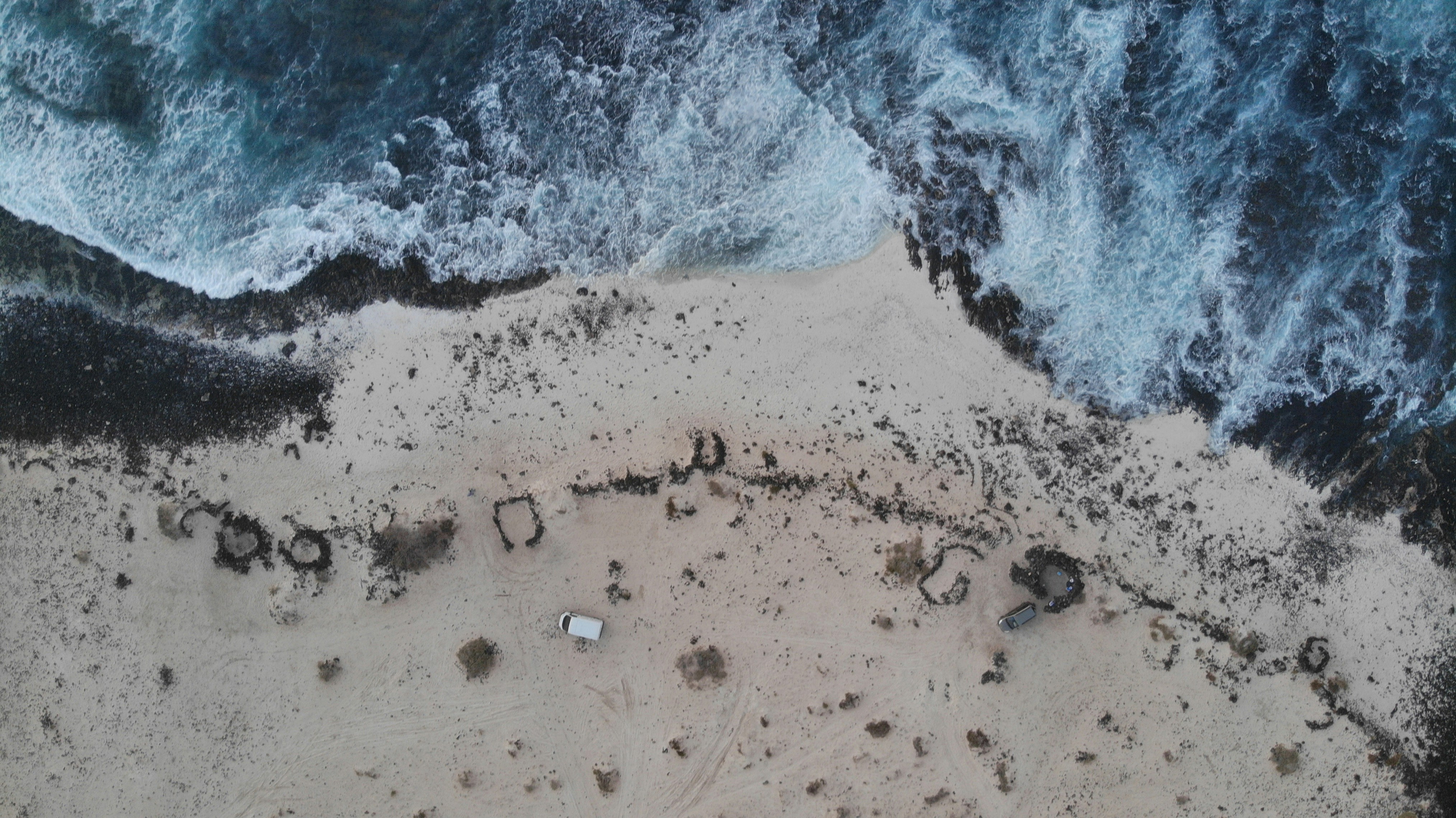Aerial view of ocean waves crashing onto a sandy beach with scattered rocks.